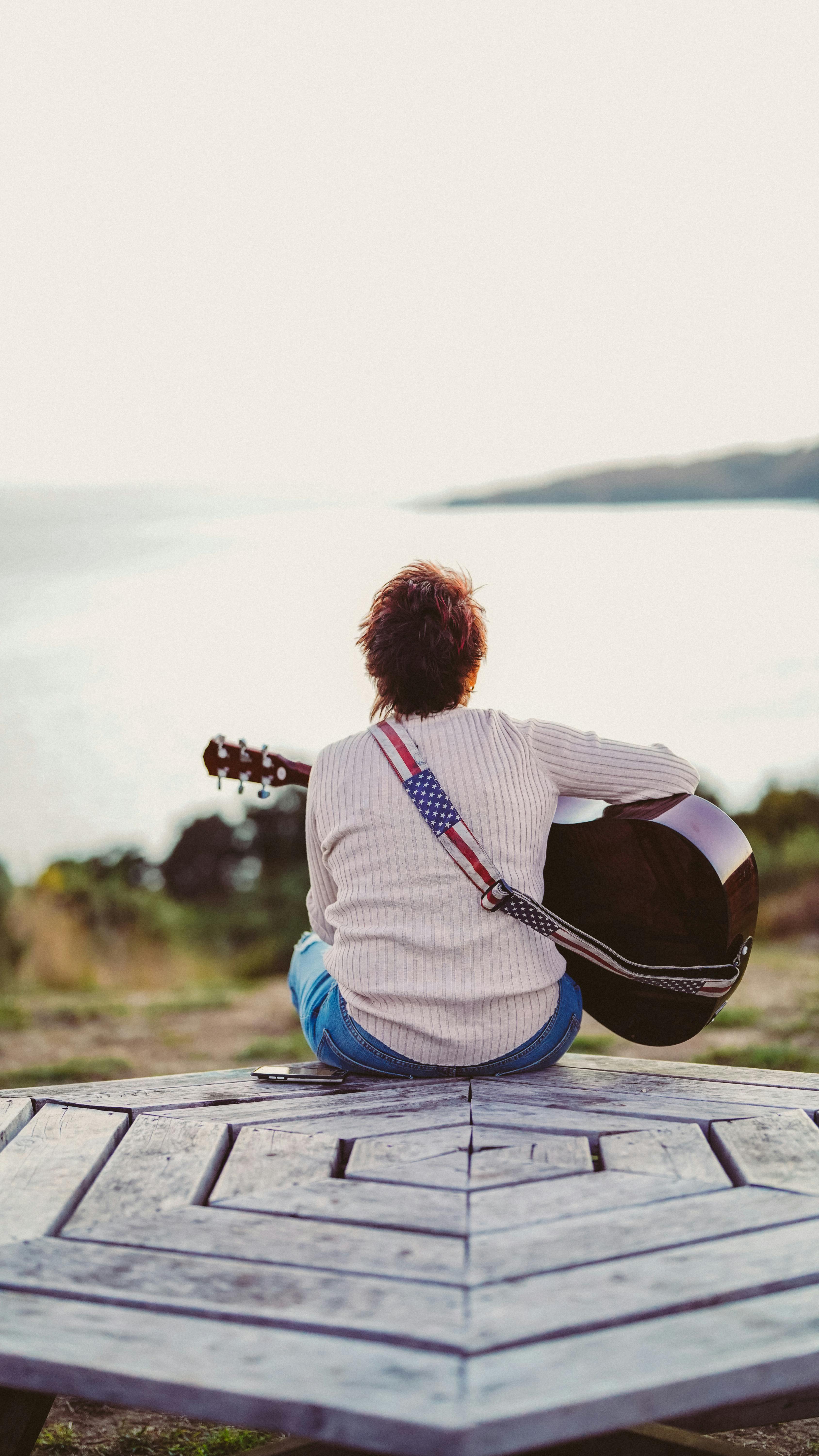 A Back View of a Person Sitting while Playing Guitar · Free Stock Photo