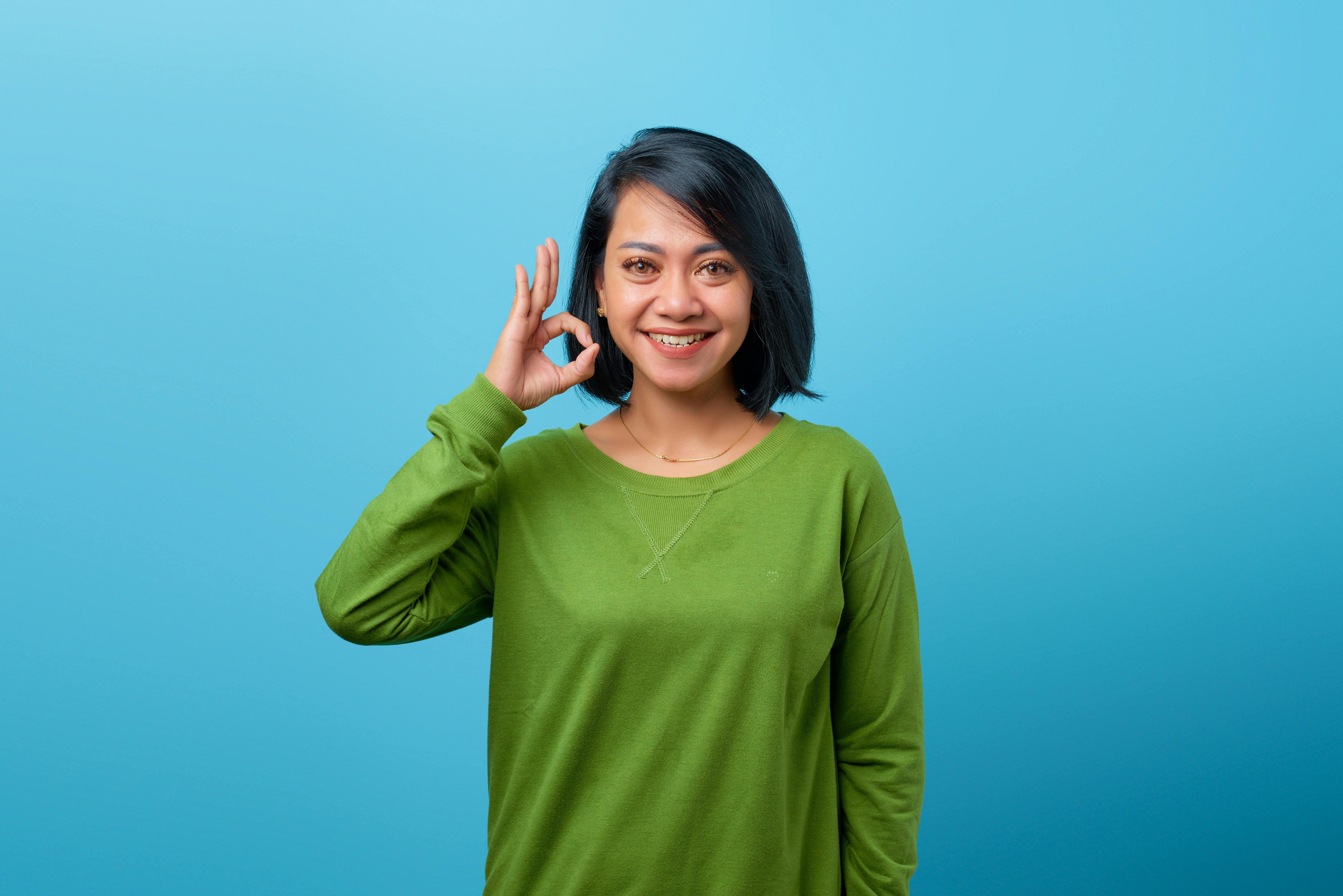 Woman in Green Long Sleeves Shirt Doing a Hand Sign · Free Stock Photo
