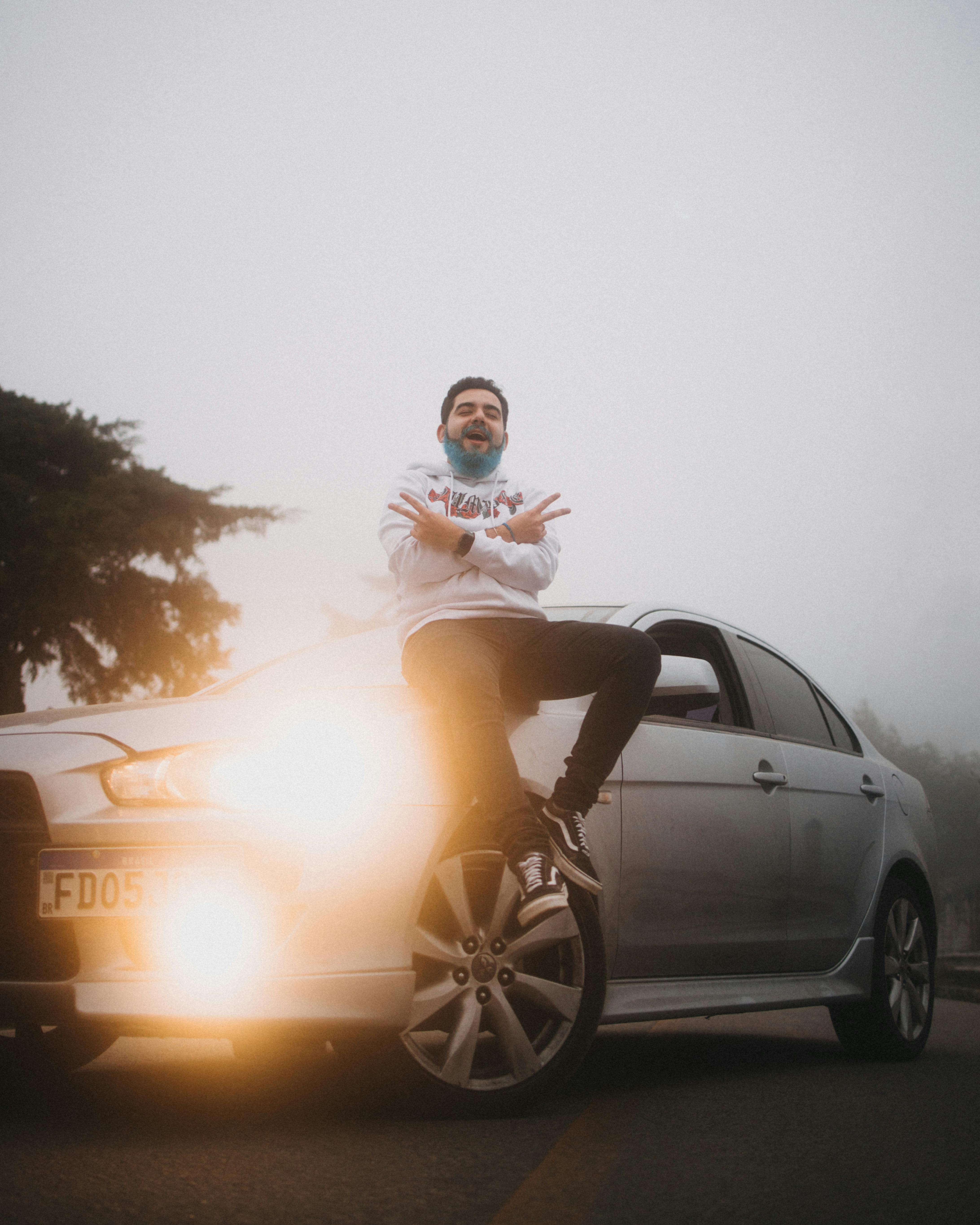 A Man Makes the Peace Sign while Sitting on the Hood of a Silver Car ...