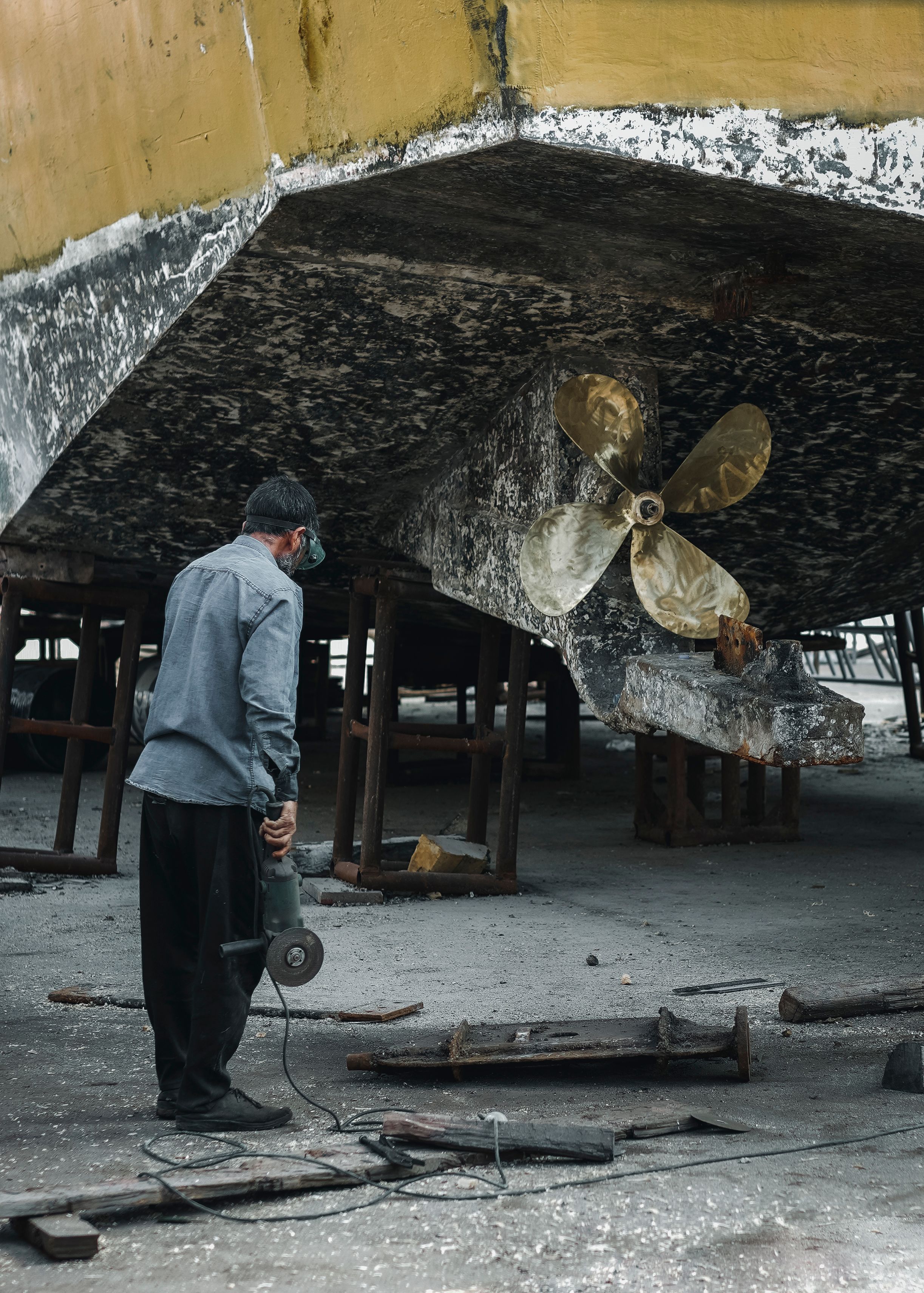 Shipyard Worker with an Angle Grinder by the Propeller of a Ship in Dry ...