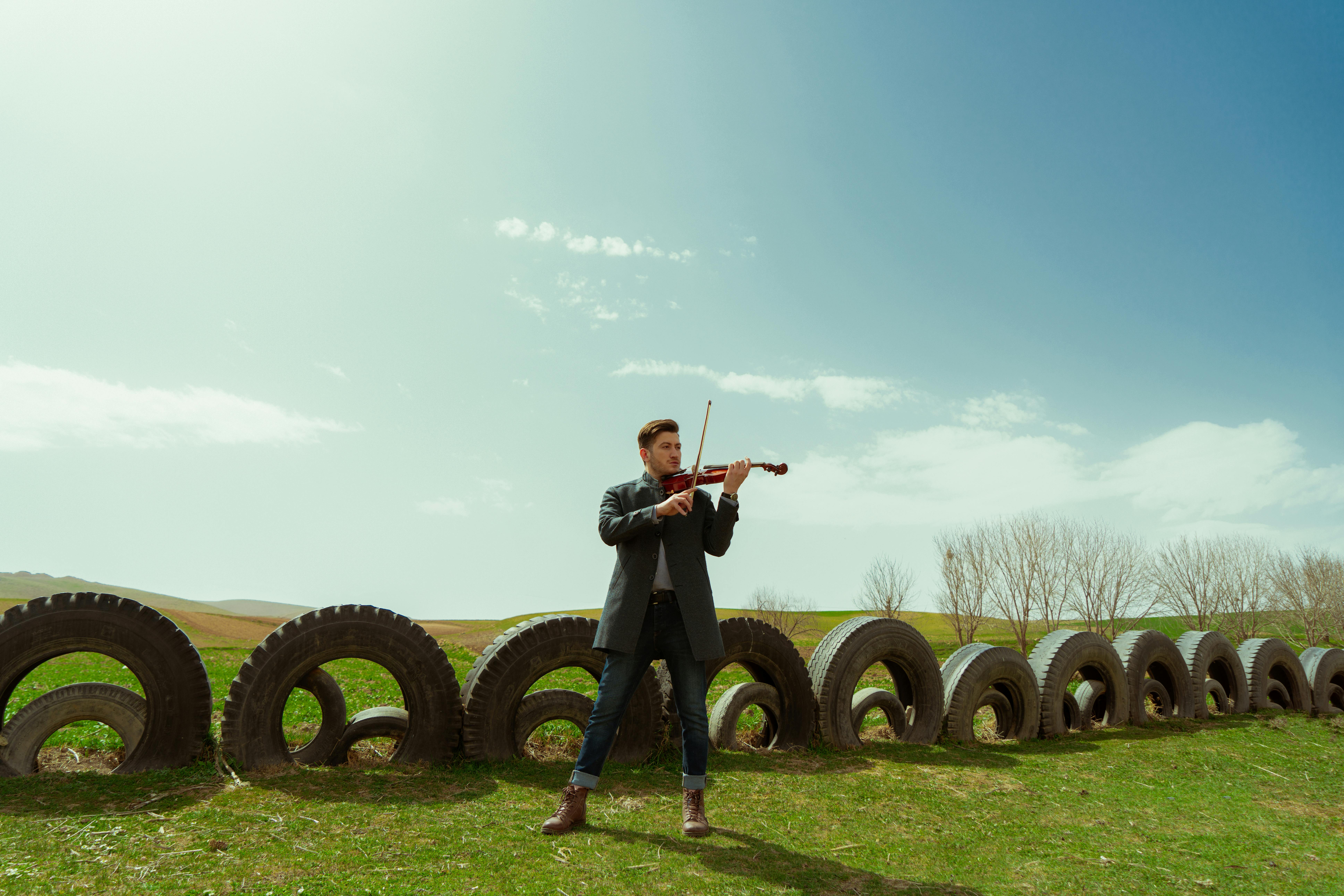 Photograph of a Man Playing a Violin Near Tires · Free Stock Photo