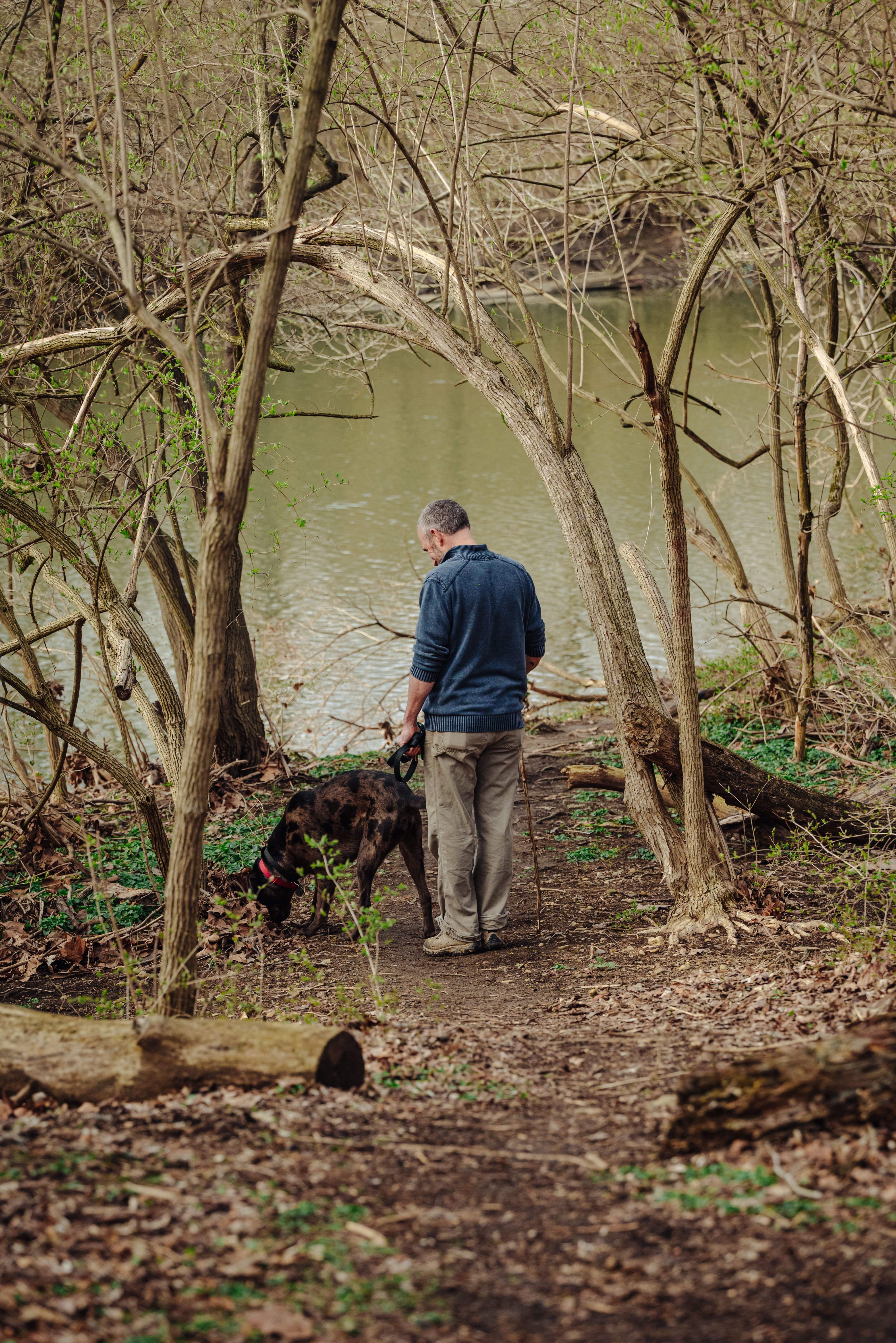 Man Holding a Dog Near Trees In Front of a Lake · Free Stock Photo