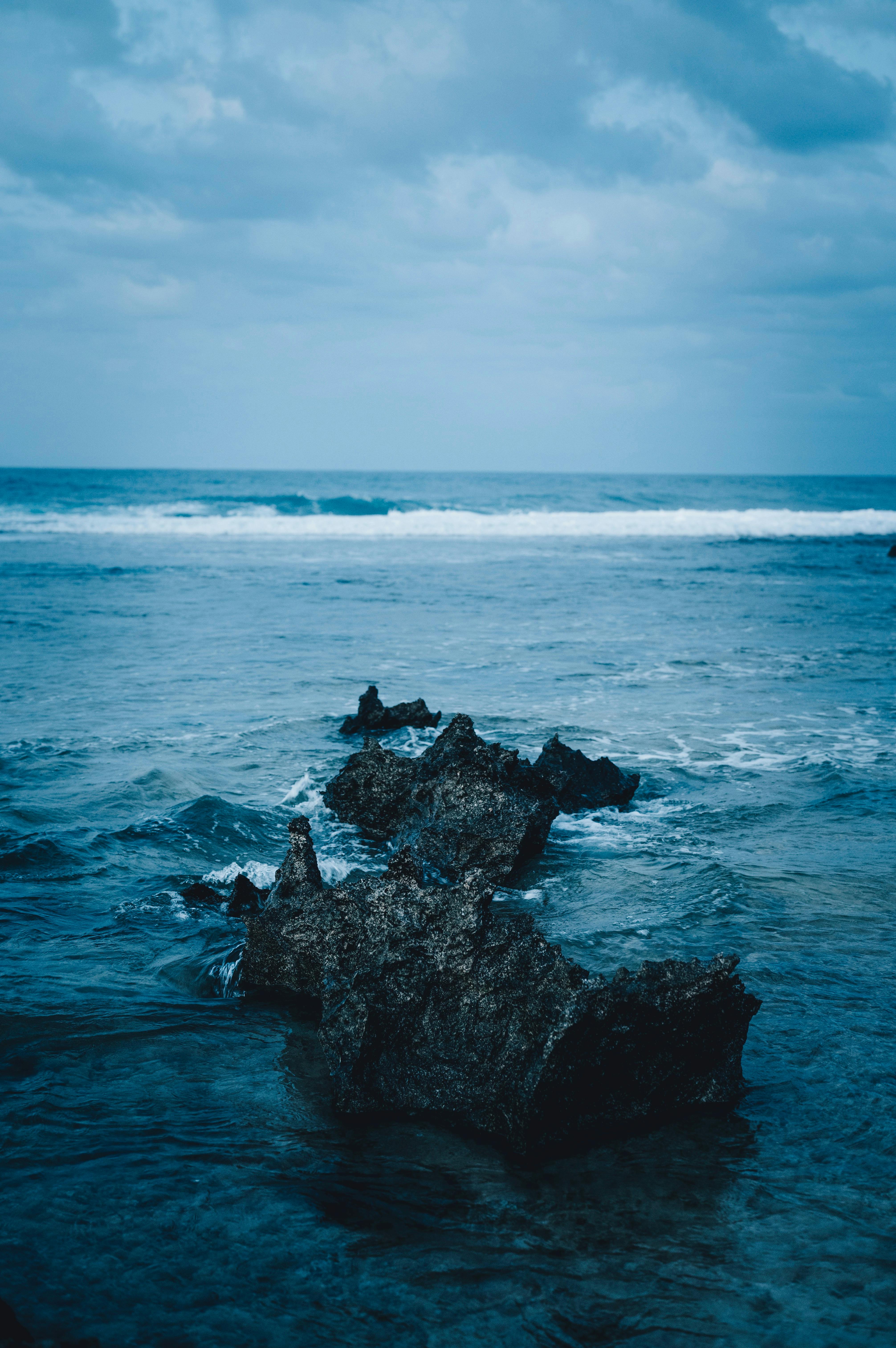 Black Rock Formation on Sea Under Blue Sky · Free Stock Photo