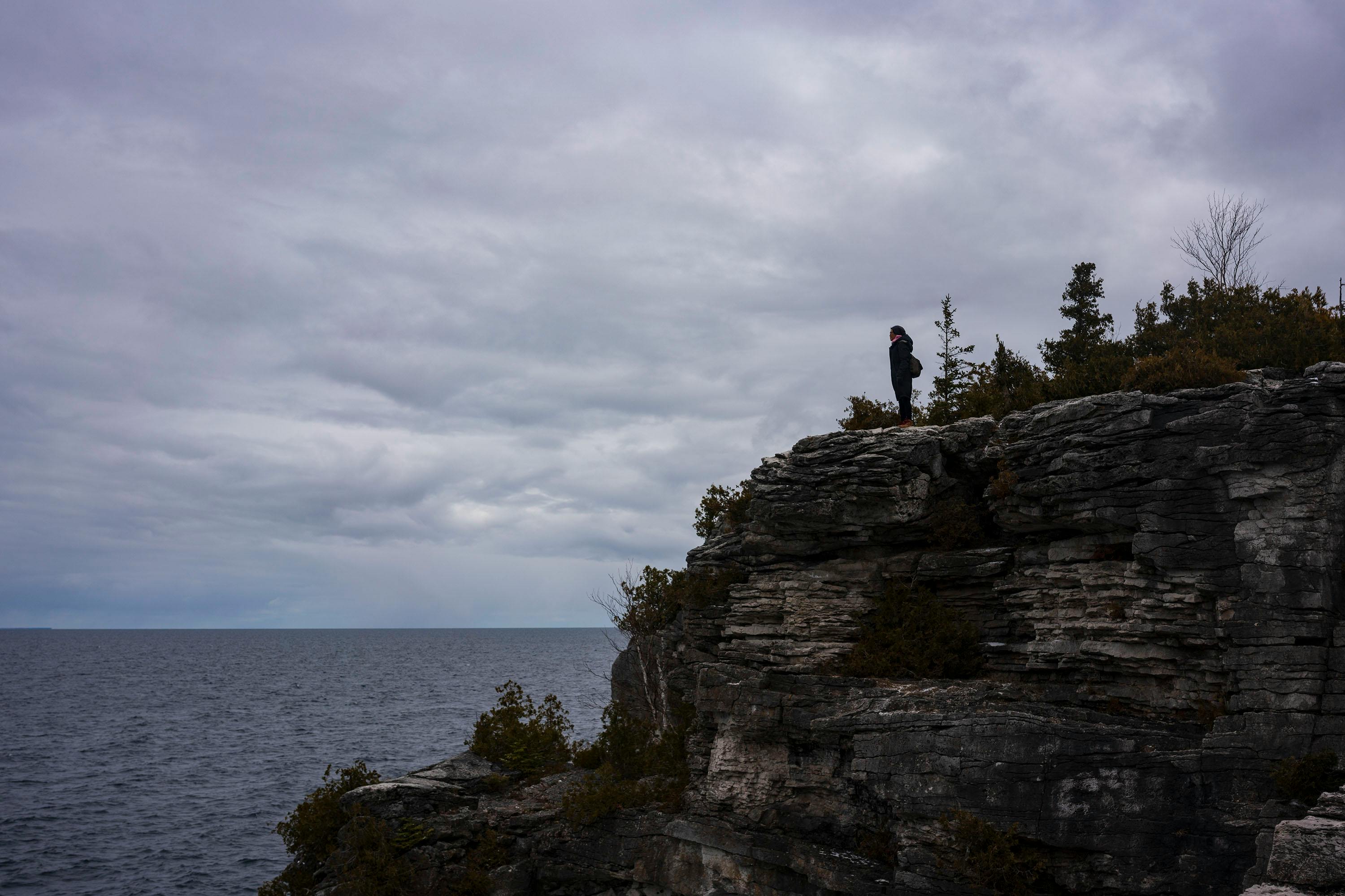 Person Standing on Mountain Cliff Under Cloudy Sky · Free Stock Photo