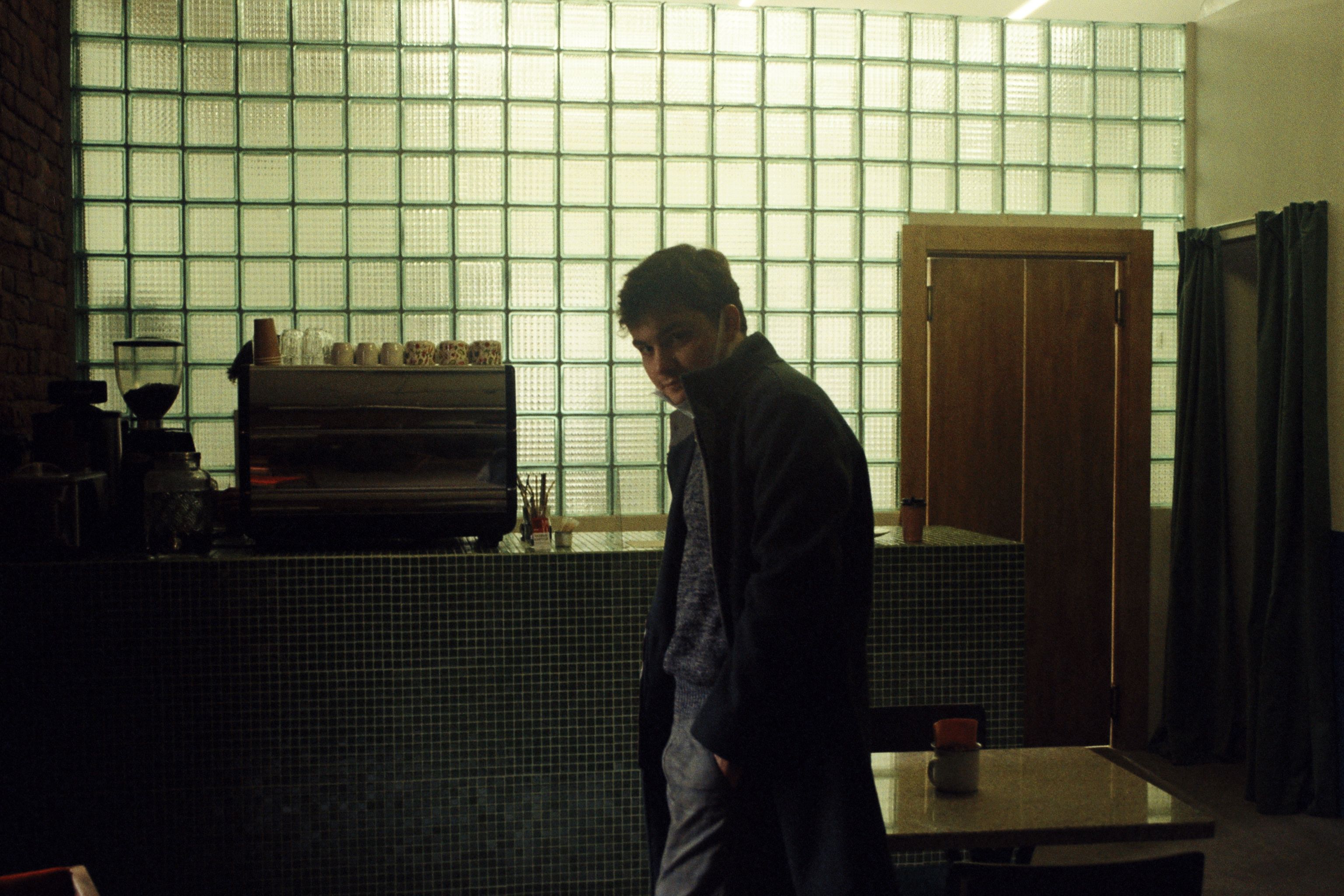 Young Man in Coat Leaning His Forehead Against Wall in Cafeteria · Free ...