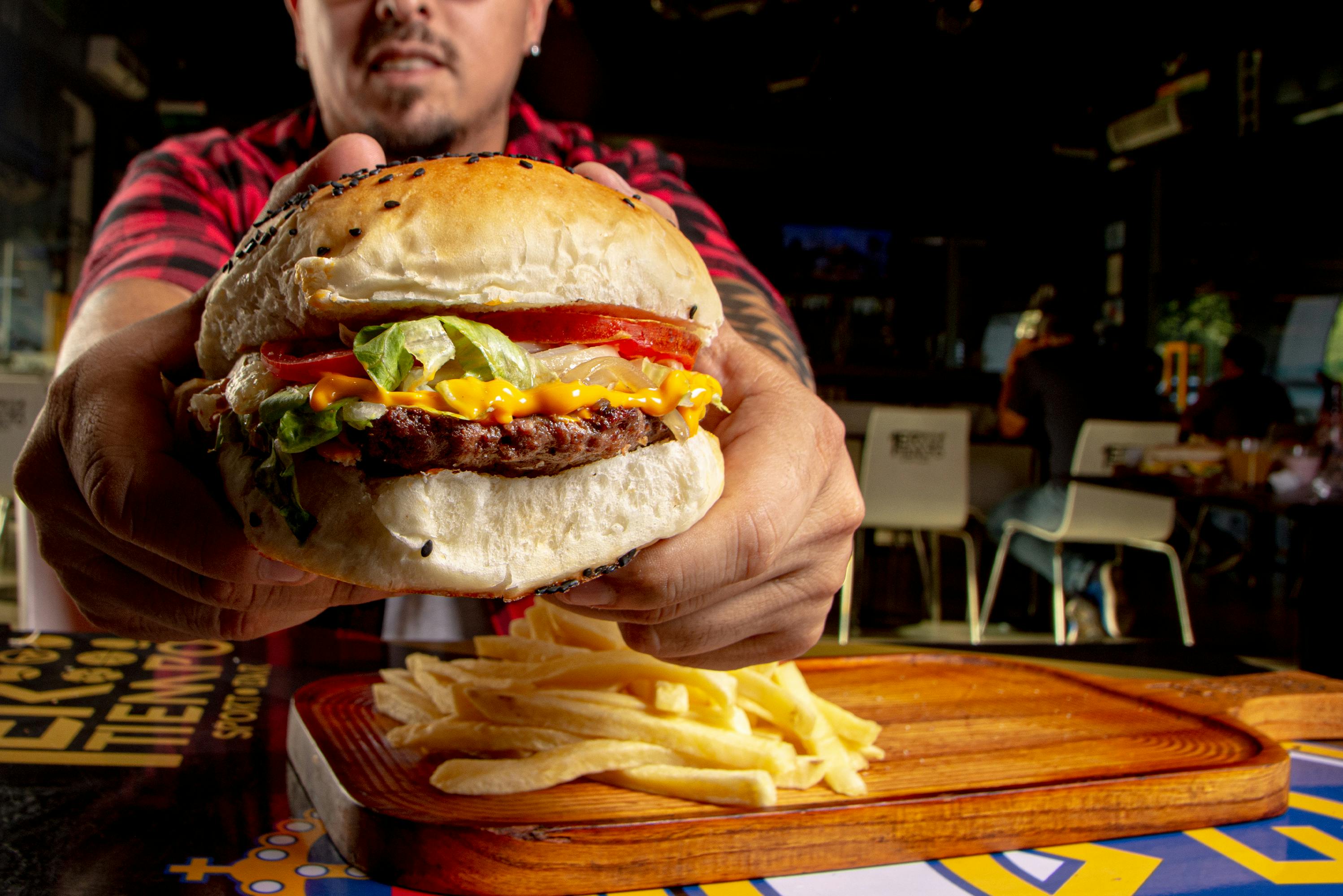 A Man Holding Delicious Cheeseburger Beside French Fries on a Wooden ...