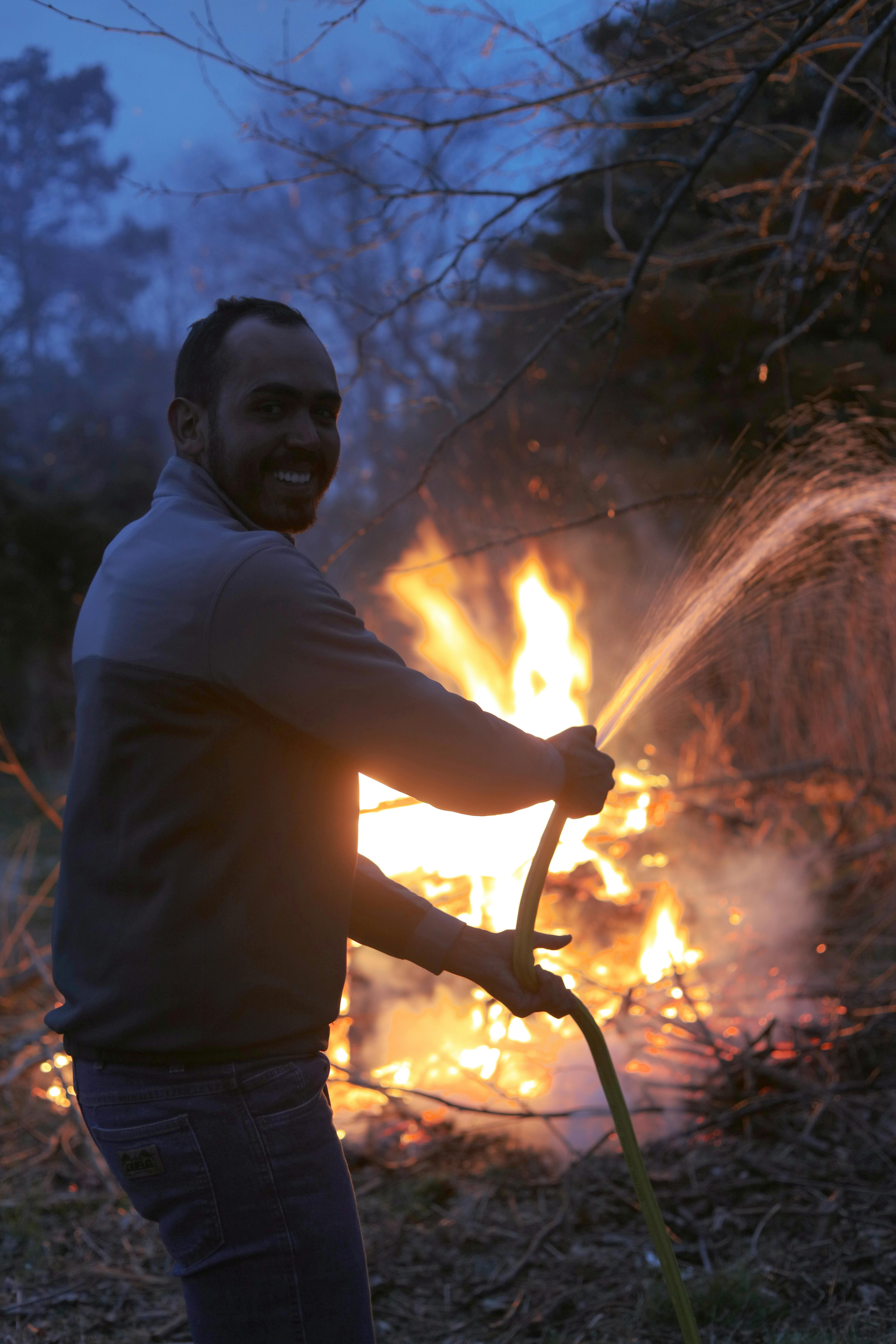 A Man Smiling Holding a Water Hose Extinguishing Fire · Free Stock Photo