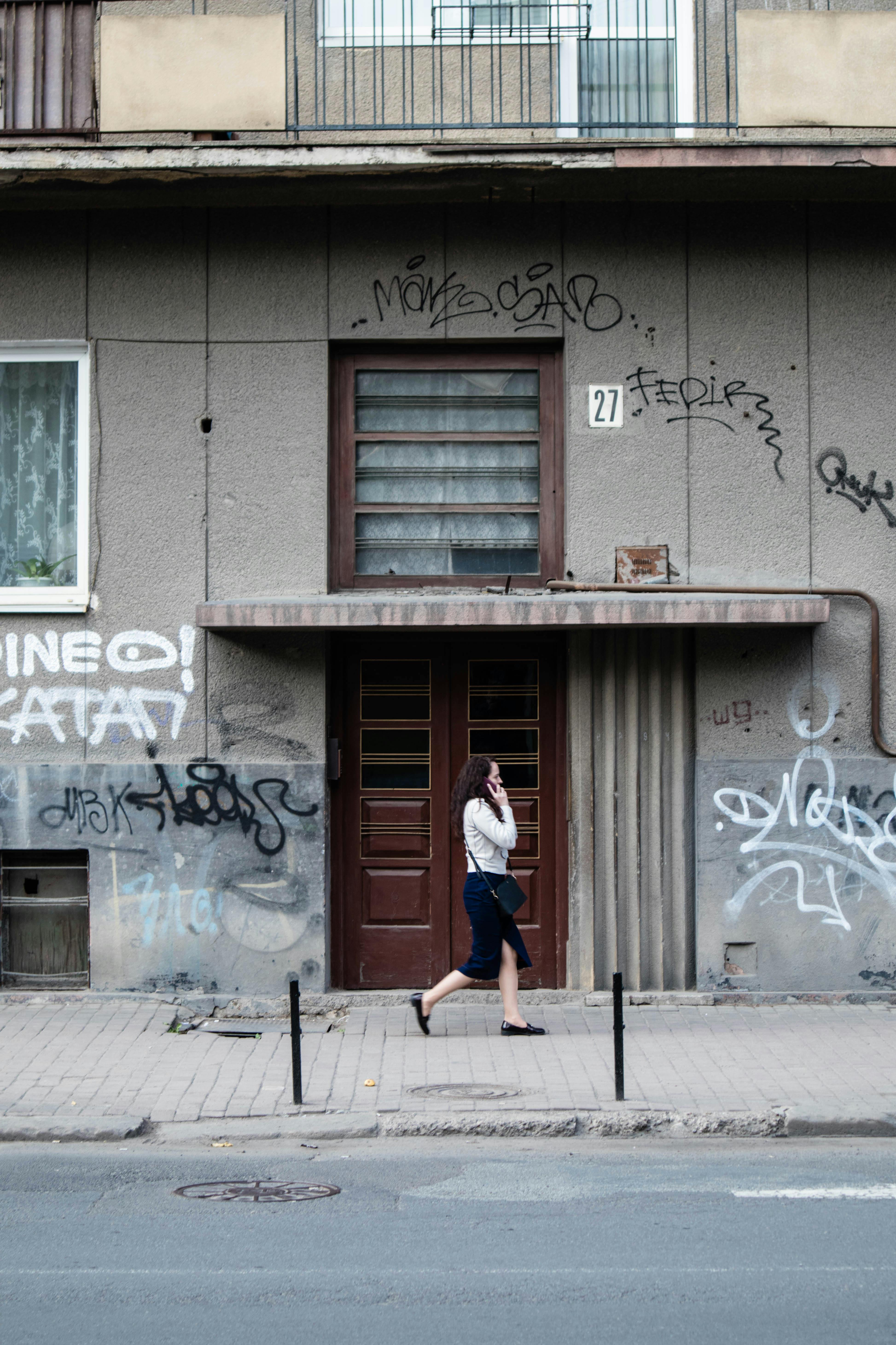 Woman Walking outside a Building with Vandalized Wall · Free Stock Photo