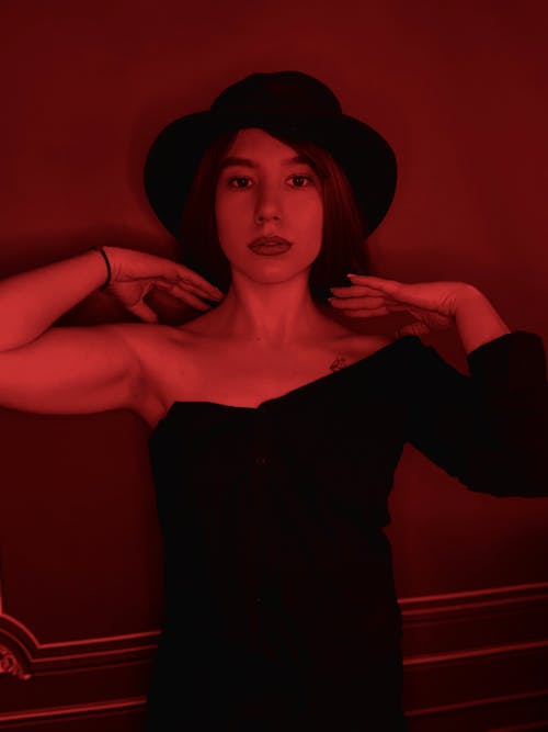 A Woman In Black Open Back Dress Wearing Black Hat Sitting On Black
