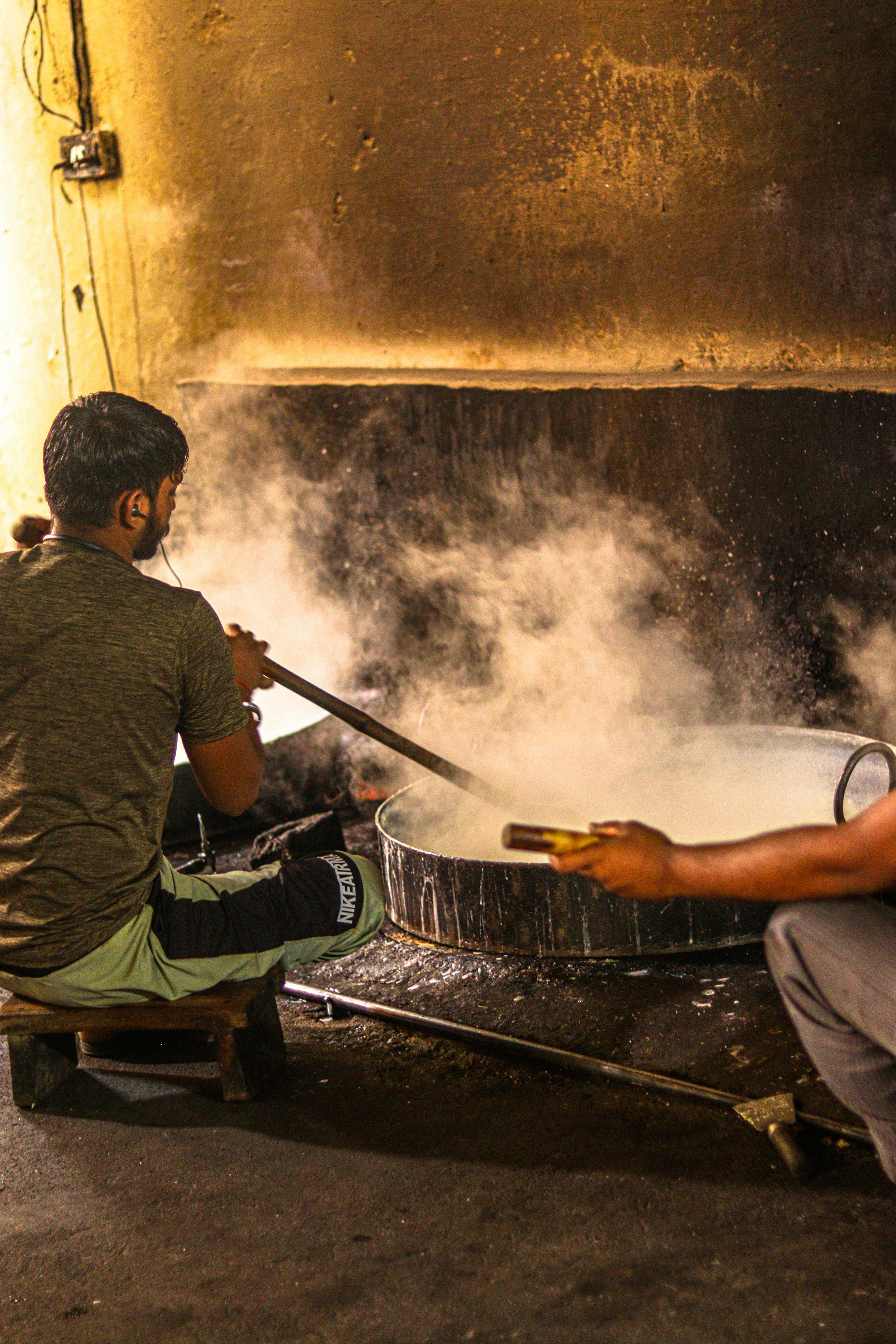 Man Cooking while Sitting on a Wooden Stool · Free Stock Photo