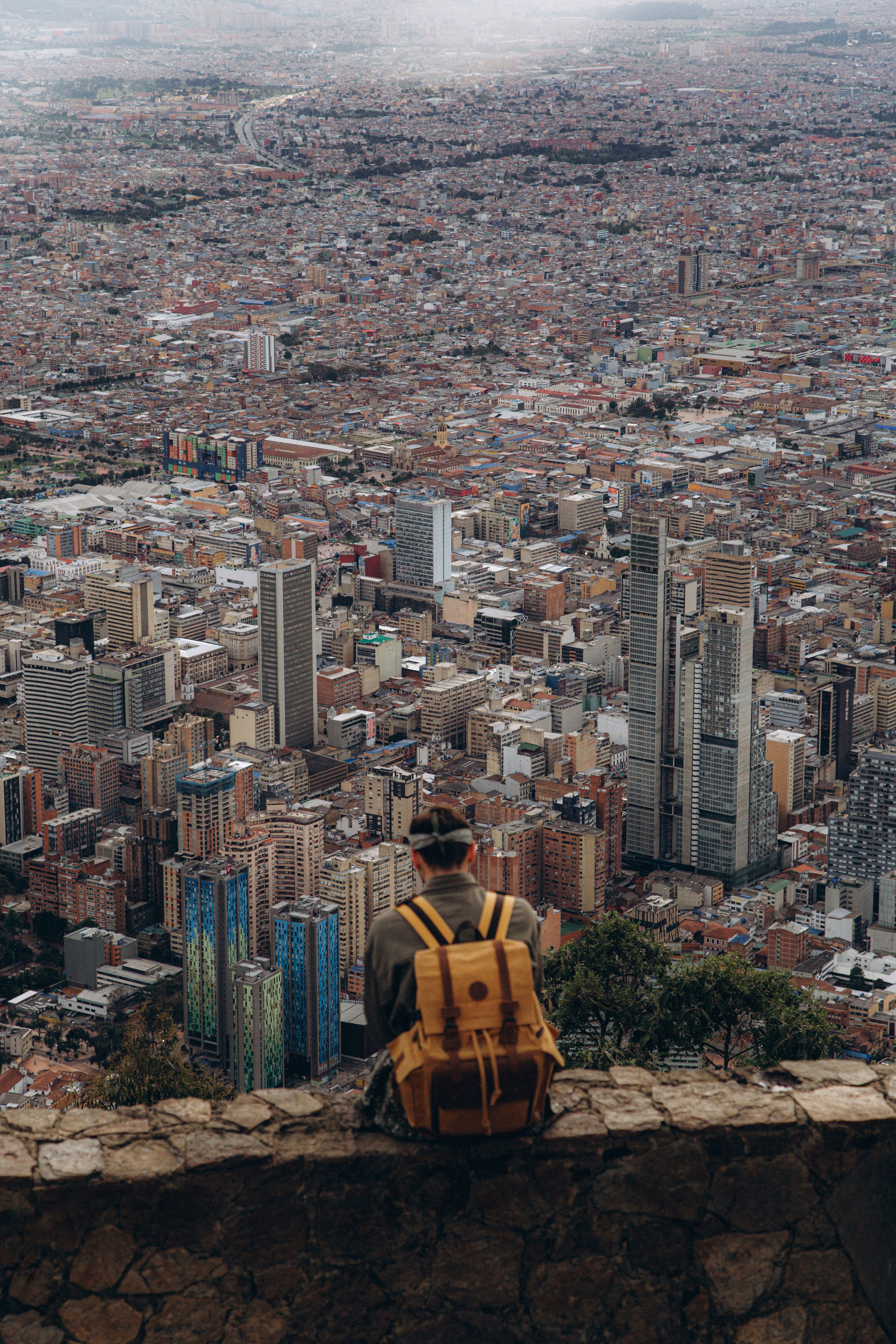 Man Sitting on a Cliff with City View · Free Stock Photo