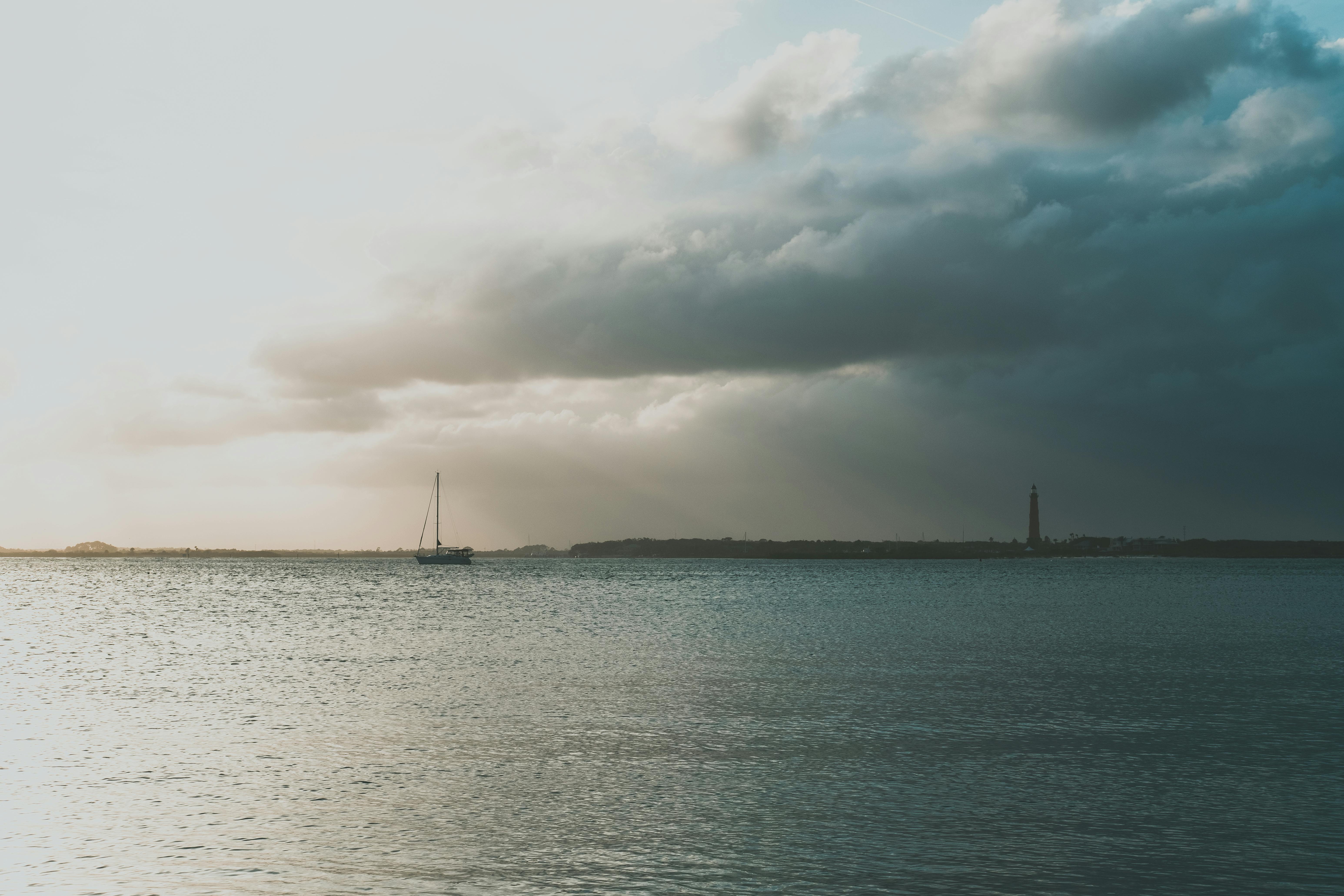 Sun Shining Through Clouds Over Sea With Lighthouse in Distance · Free ...