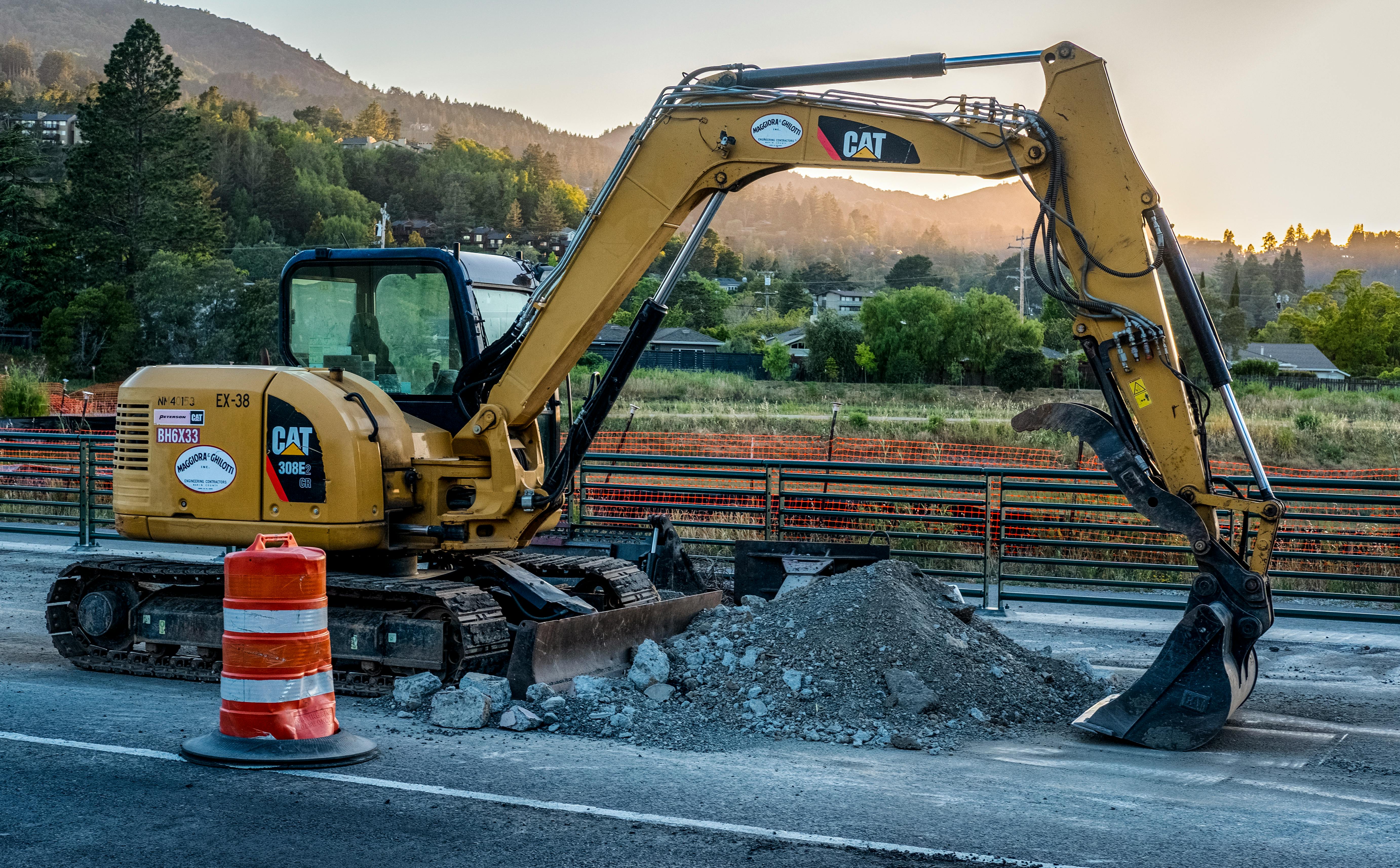 A Yellow and Black Excavator on Concrete Road with Soil and Rocks ...