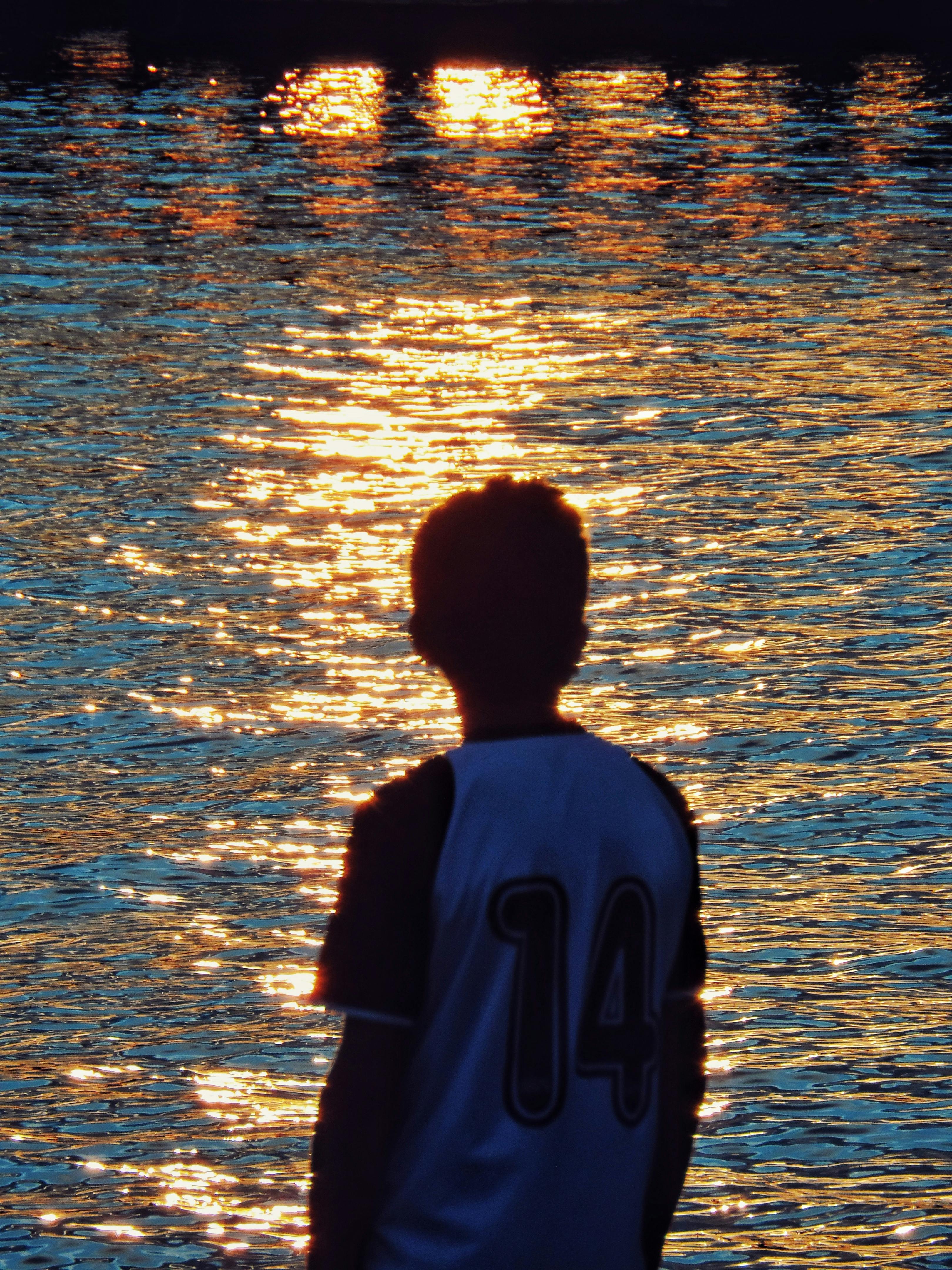 Person Standing in Front of Light Reflections on Water · Free Stock Photo