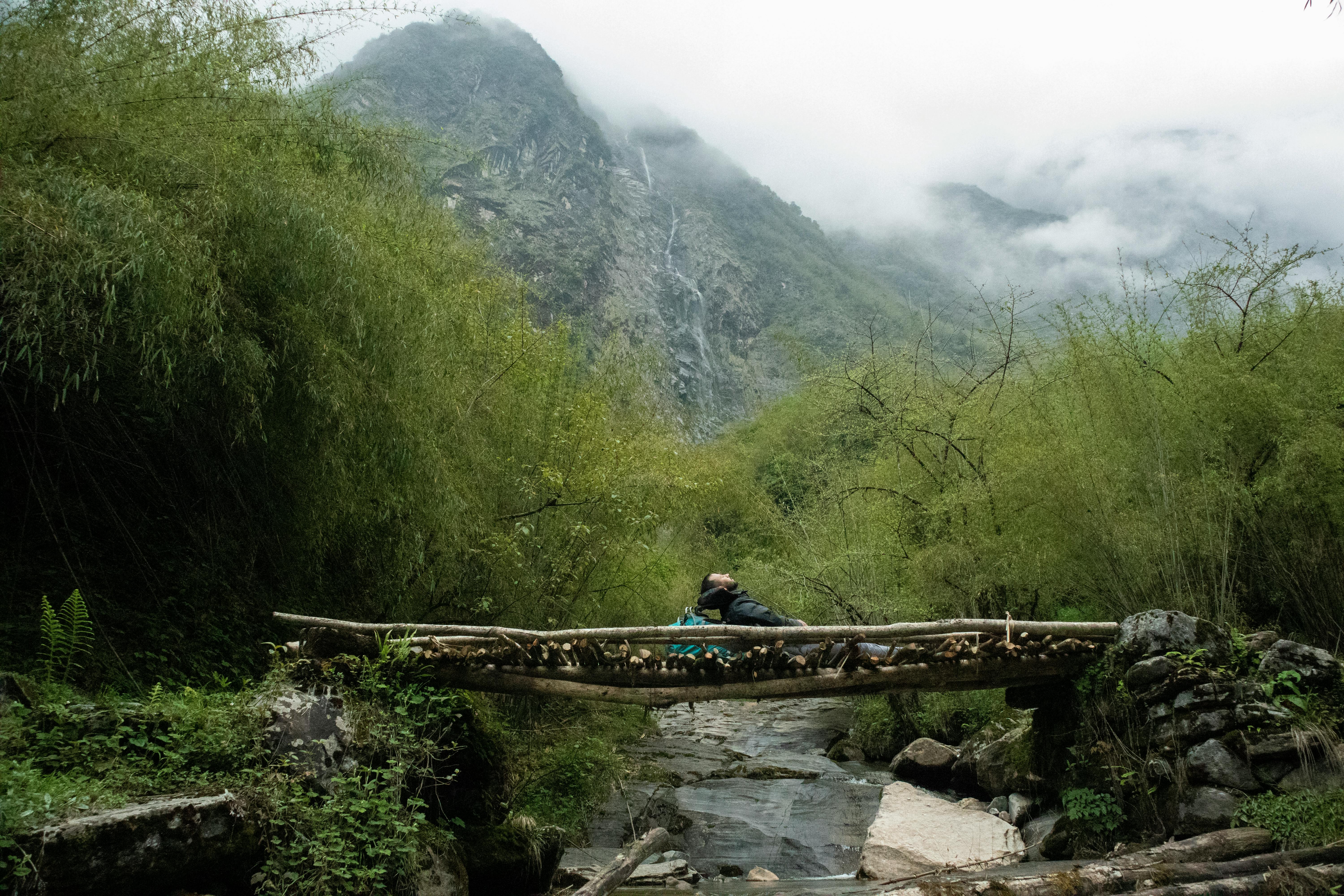 A Person Lying on the Wooden Bridge Over the Stream · Free Stock Photo