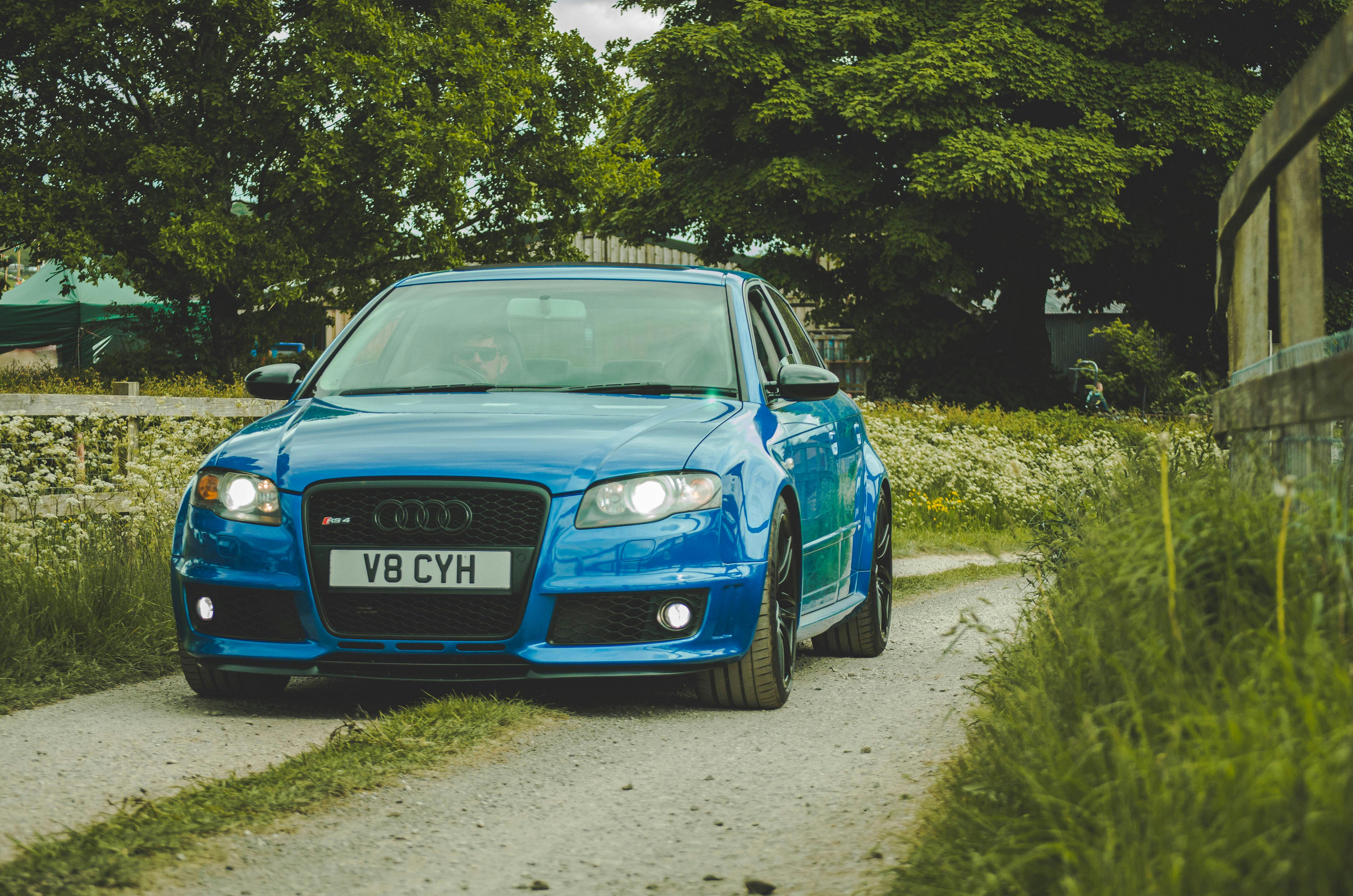 Blue Audi Car Moving on the Street Between Green Grasses · Free Stock Photo