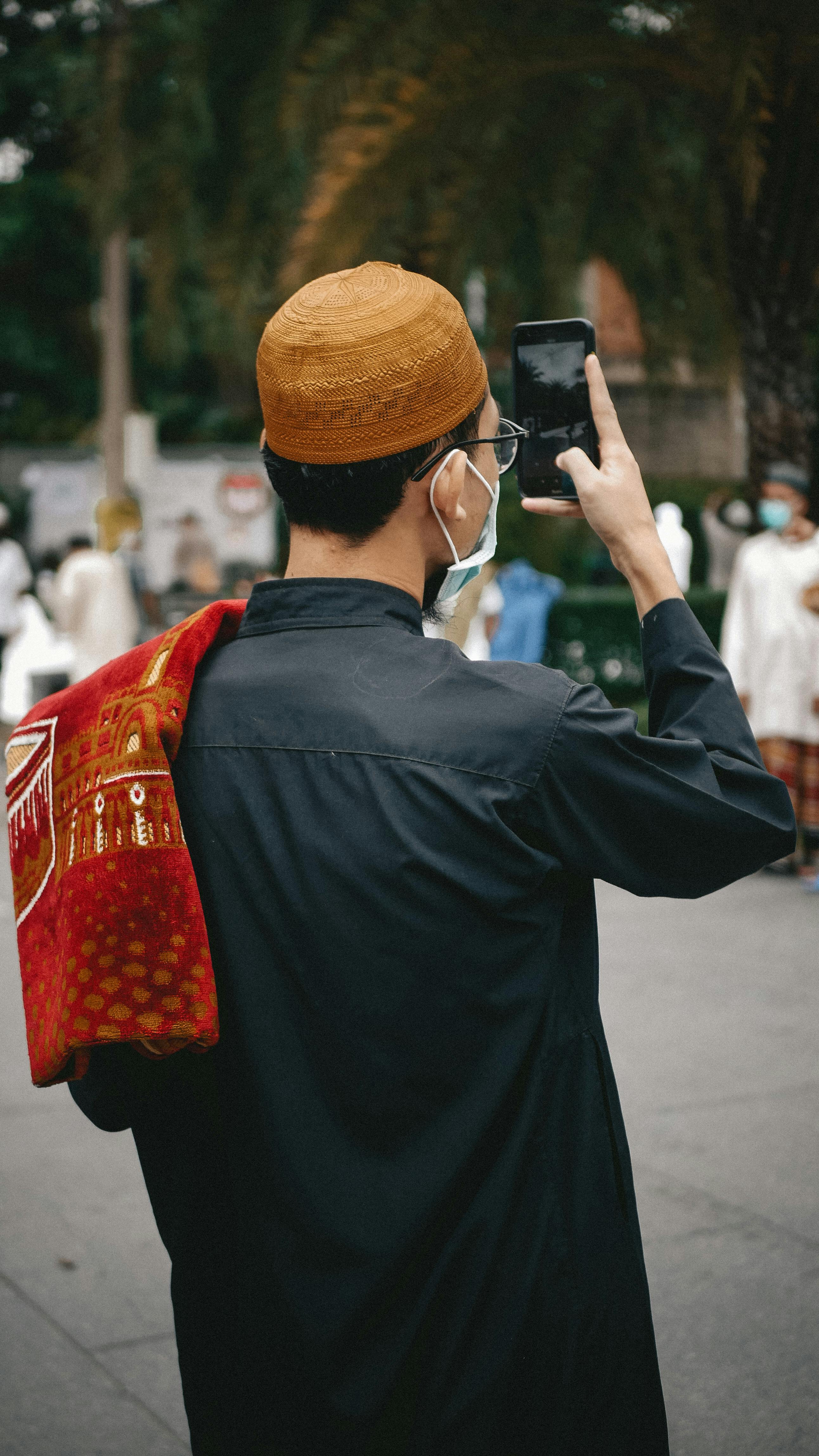 Man in Black Thobe Wearing Brown Praying Cap Standing and Using ...