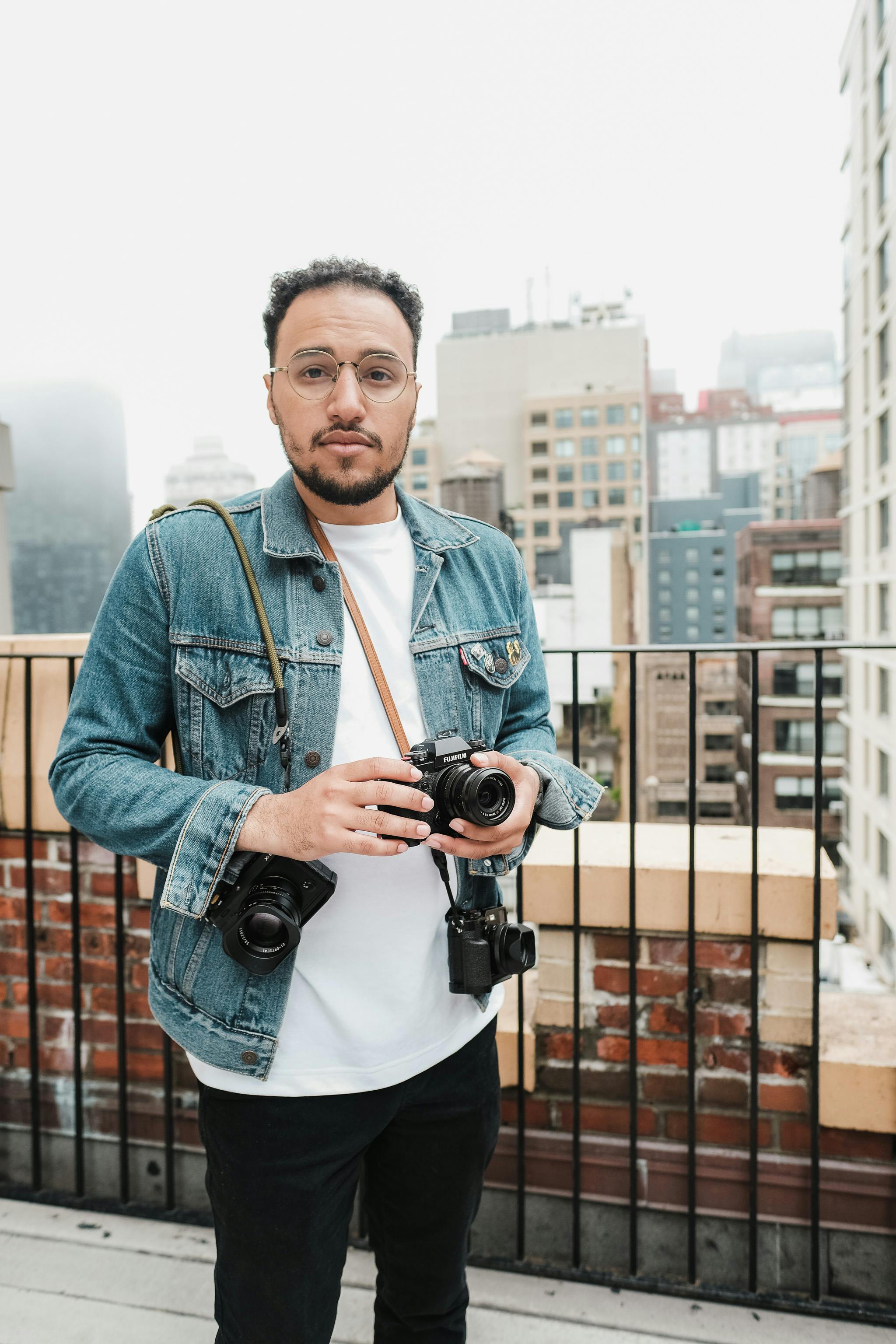 A Man in Blue Denim Jacket Holding Black Dslr Camera Behind Tall ...