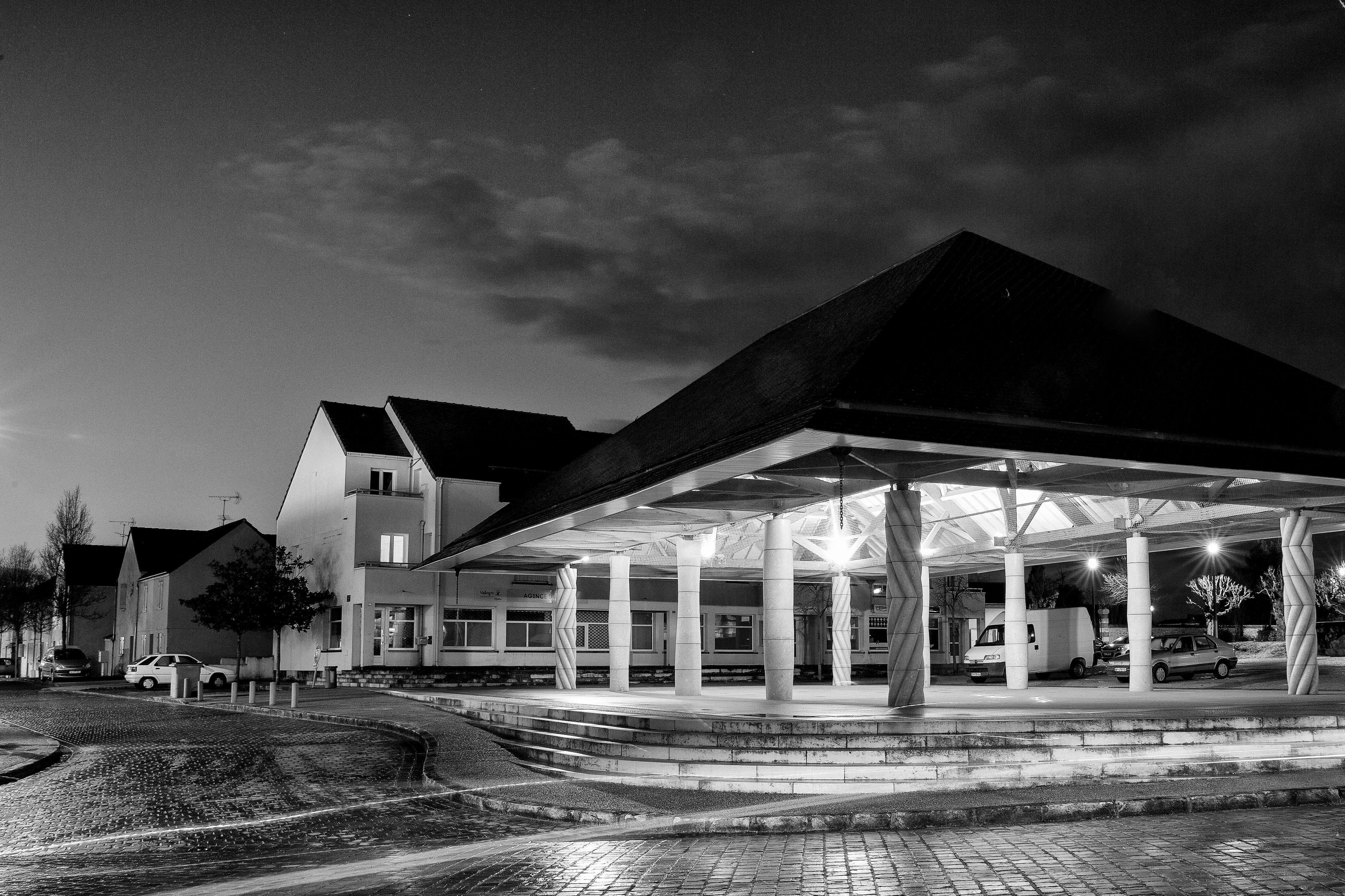 Grayscale Photo of a Gazebo Beside White Building · Free Stock Photo