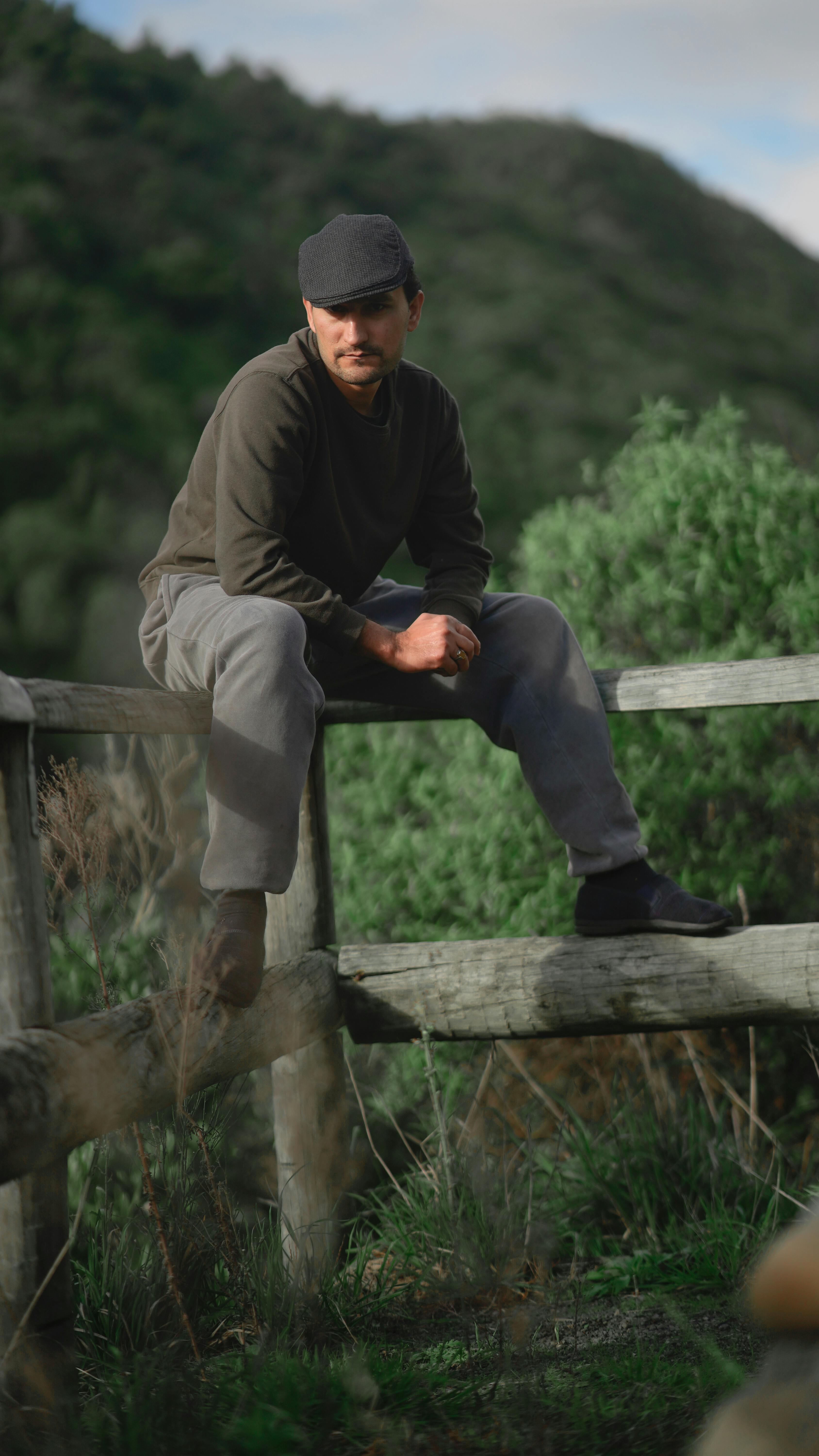 Man Sitting on Wooden Fence in Rural Landscape · Free Stock Photo