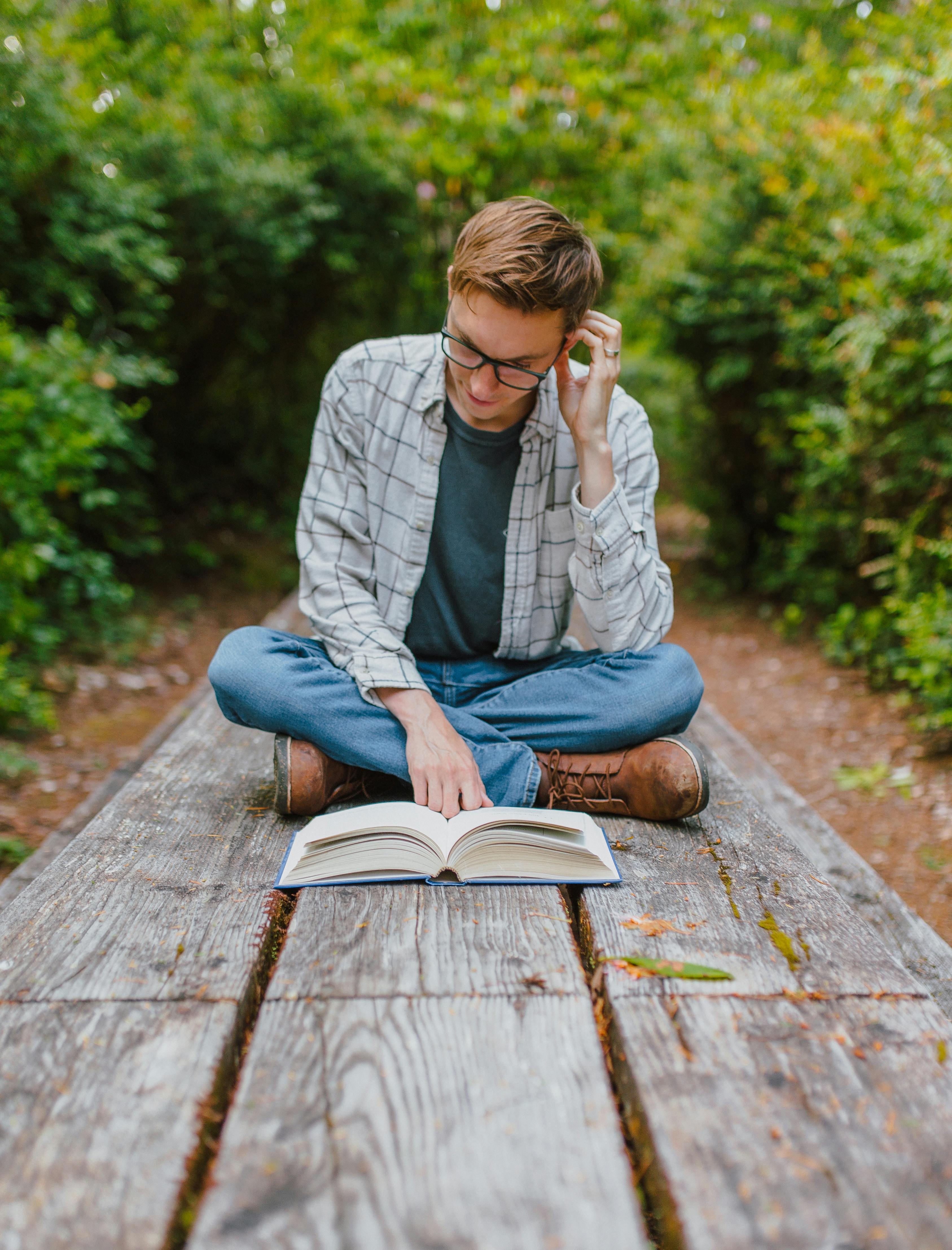 Man Sitting on Wooden Plank While Reading a Book · Free Stock Photo