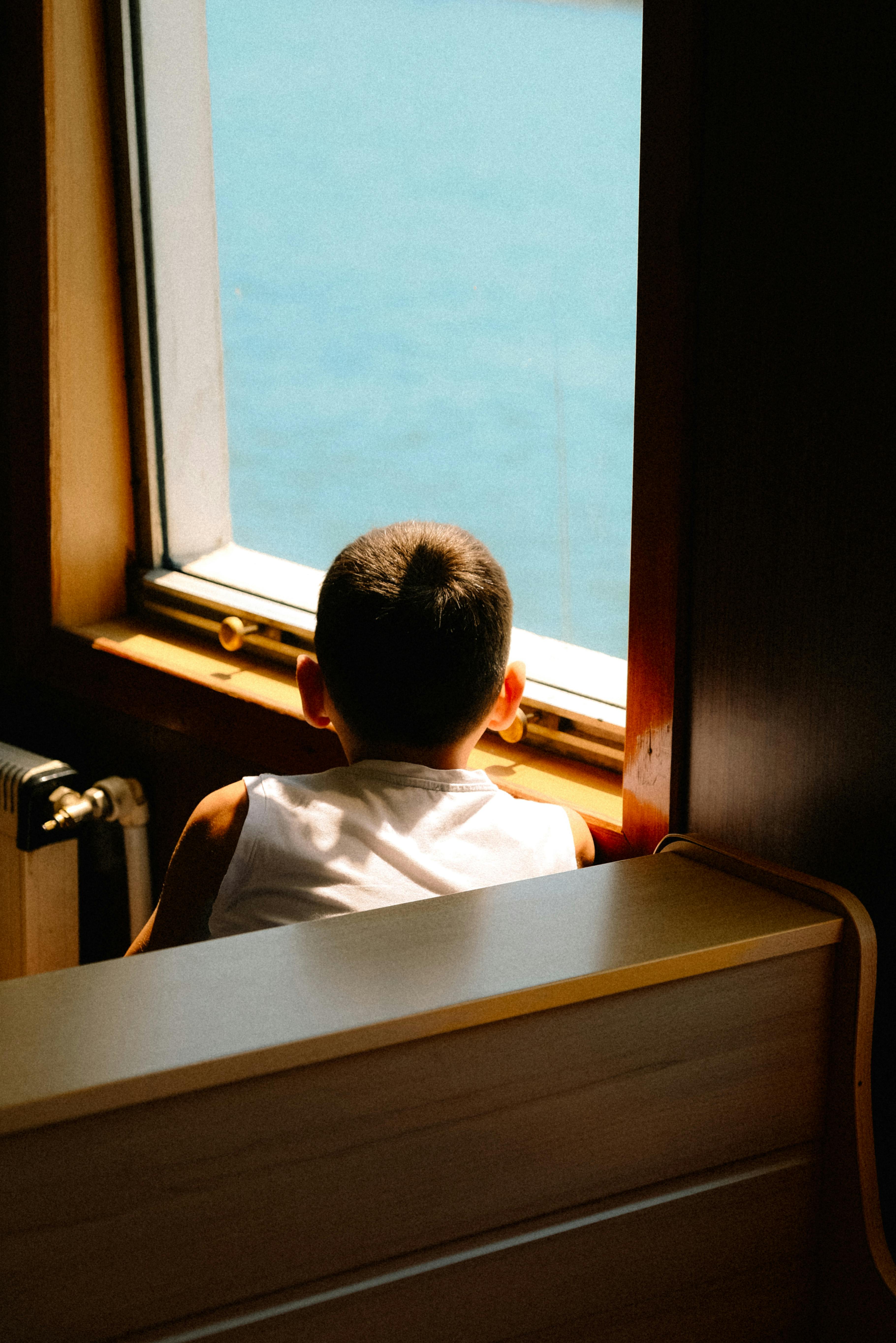 Boy in White Tank Top Sitting While Looking at the Window · Free Stock ...