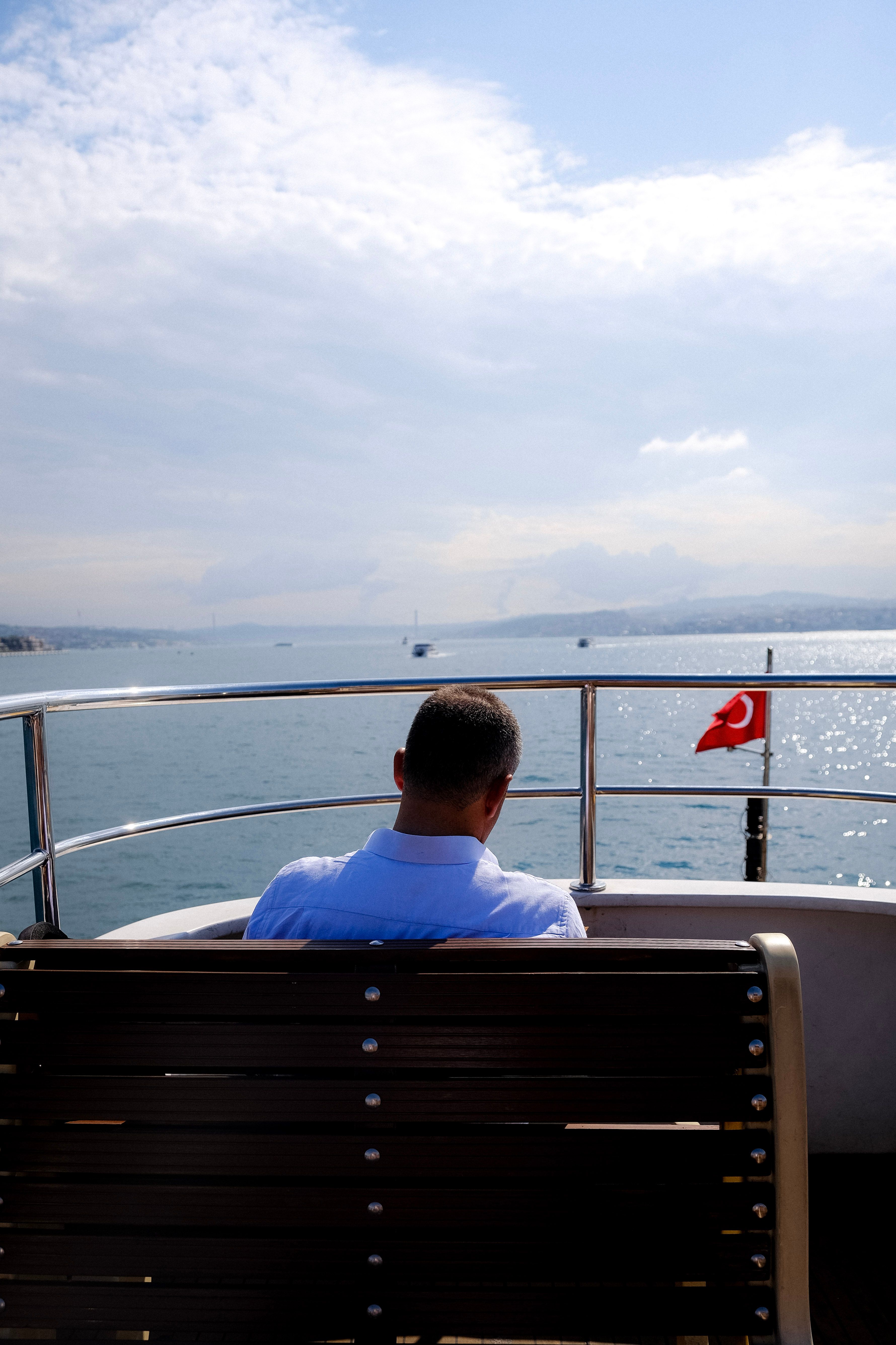 Back View of a Man Wearing a Hood, Sitting on a Ferry and Looking at ...