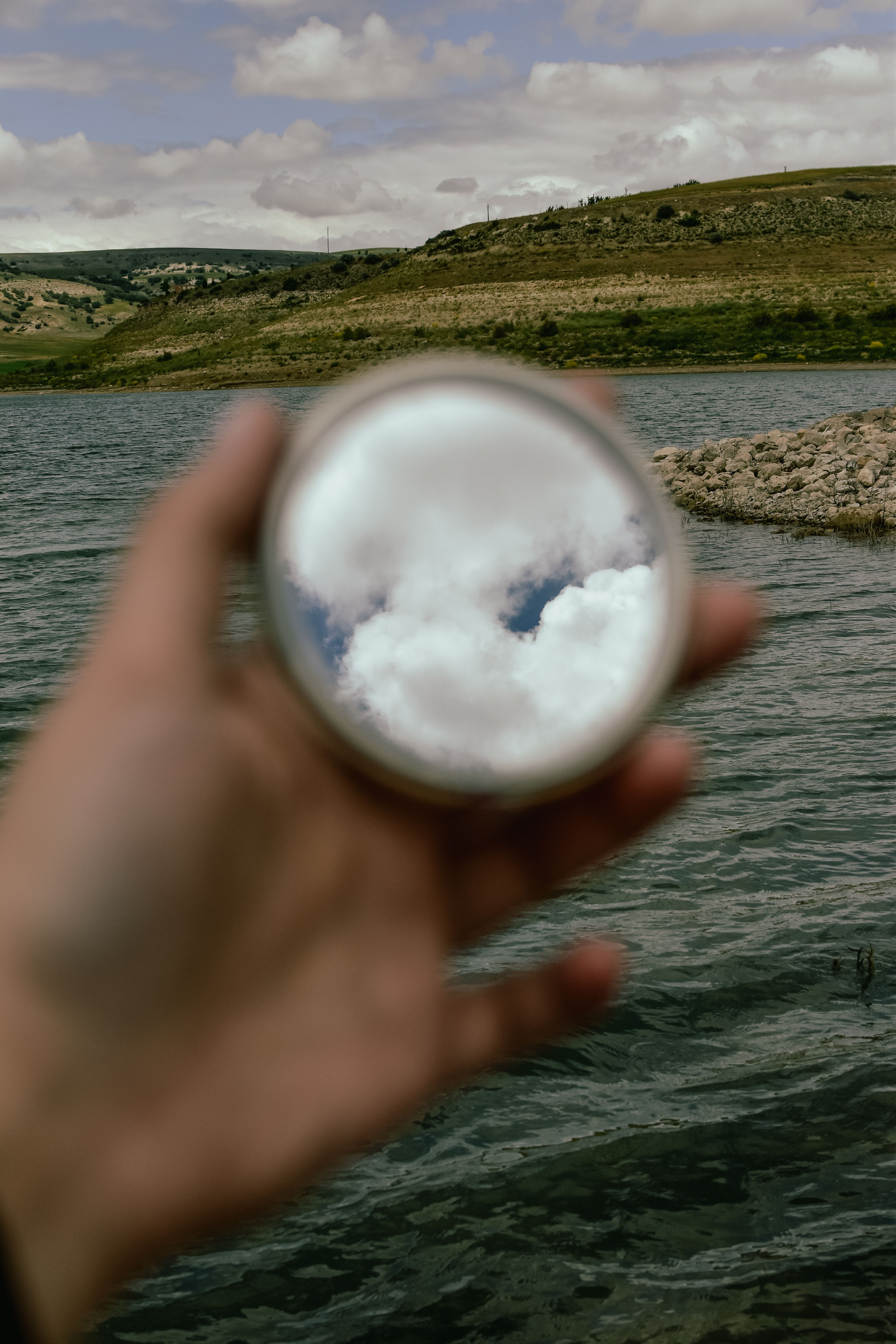 Hand Holding Mirror with Sky Reflection Against Water · Free Stock Photo