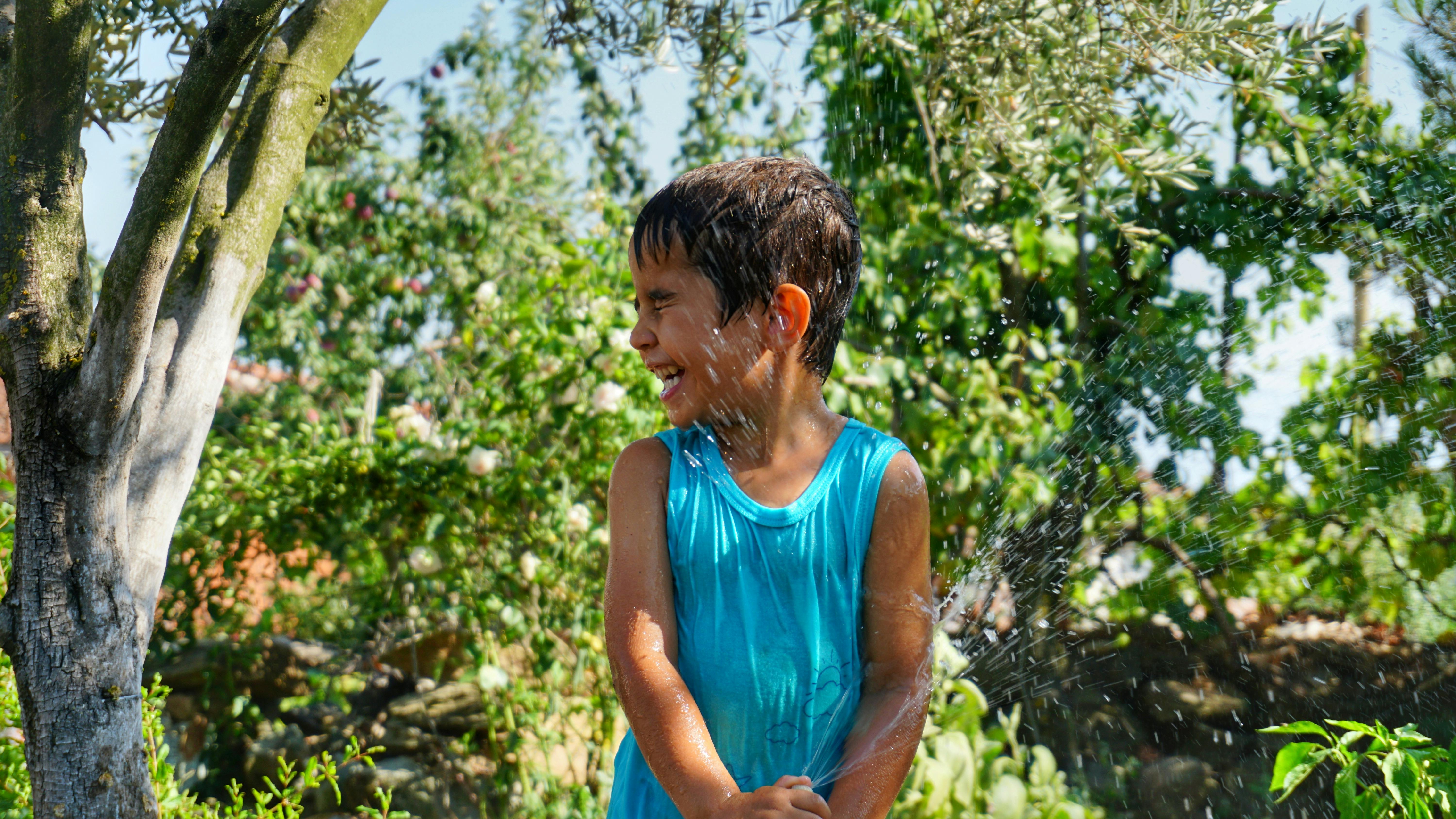 Photo of a Boy Laughing at Being Soaked in Water by a Garden Hose ...