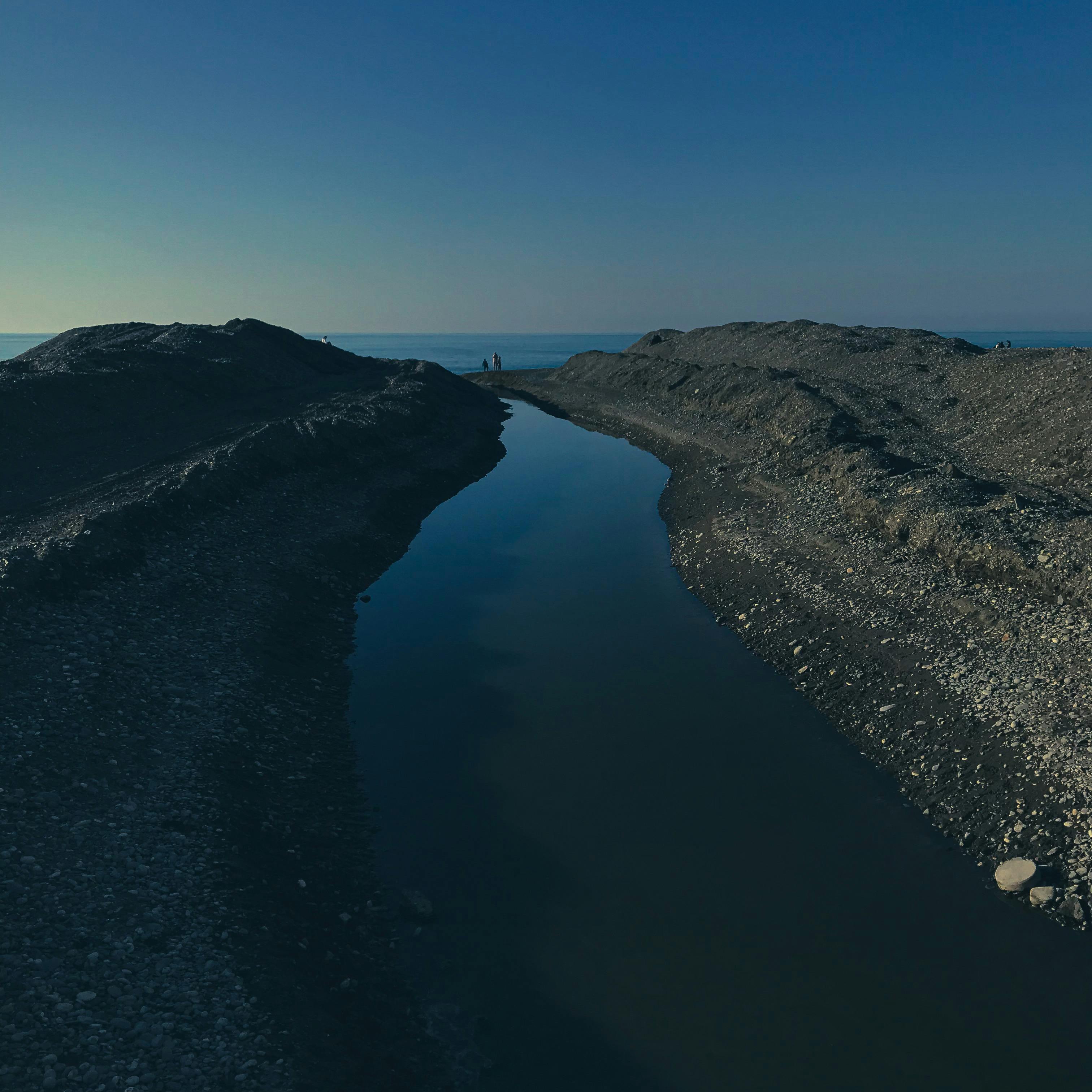 River Between Heaps of Black Gravel by the Sea · Free Stock Photo