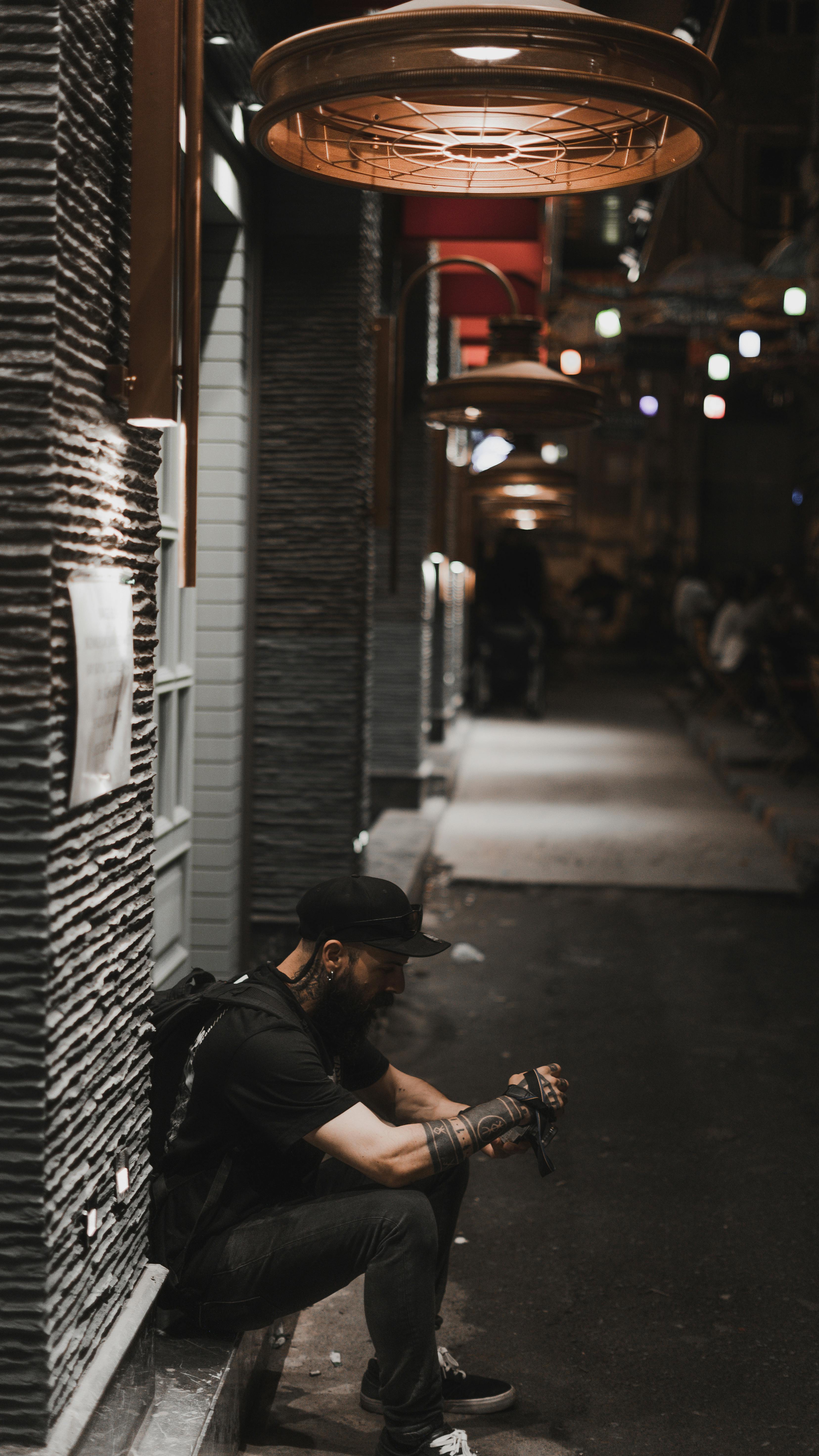 A Tattooed Man in a Black Outfit Sitting on a Sidewalk · Free Stock Photo