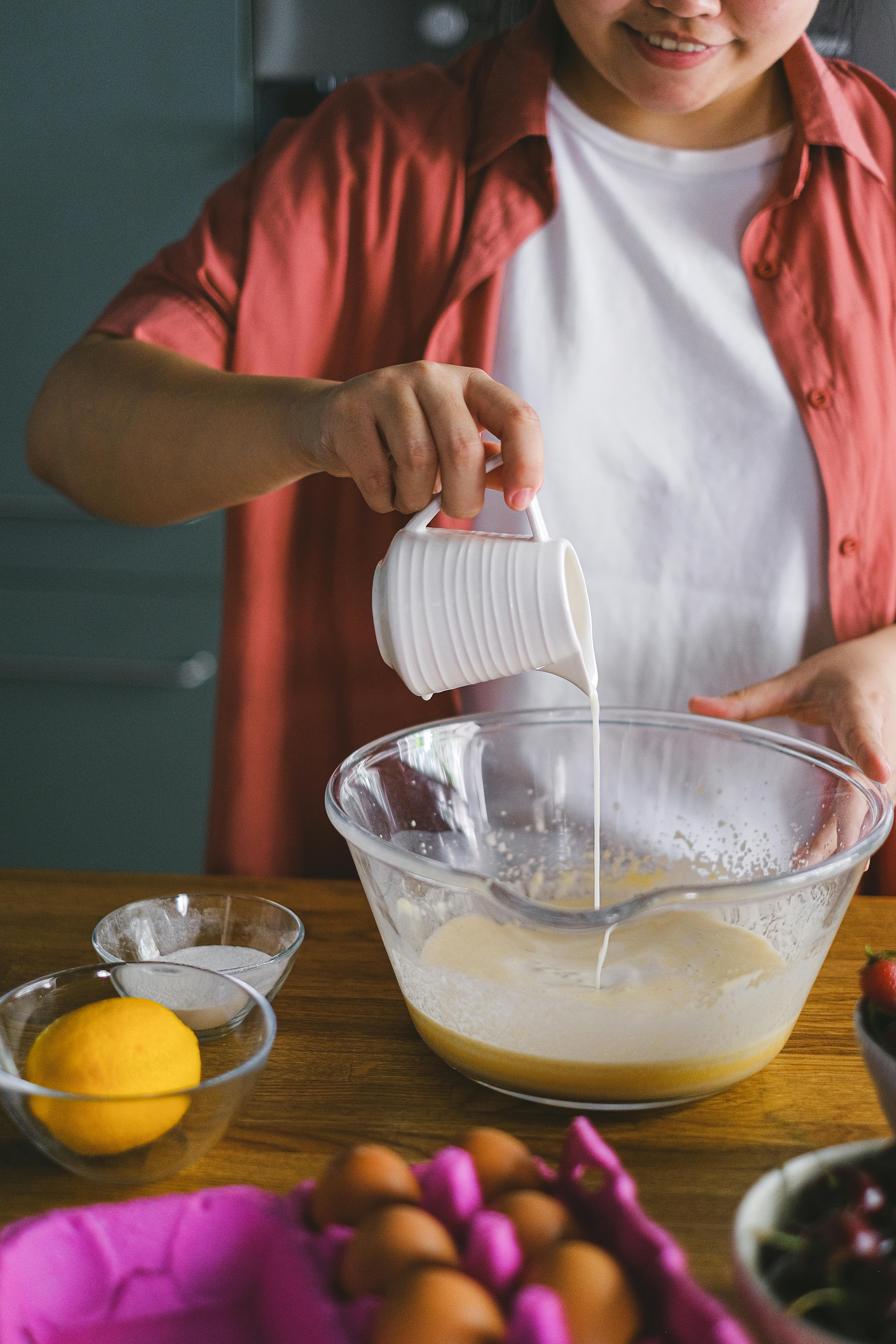 A Woman Pouring Mix in a Glass Mixing Bowl · Free Stock Photo