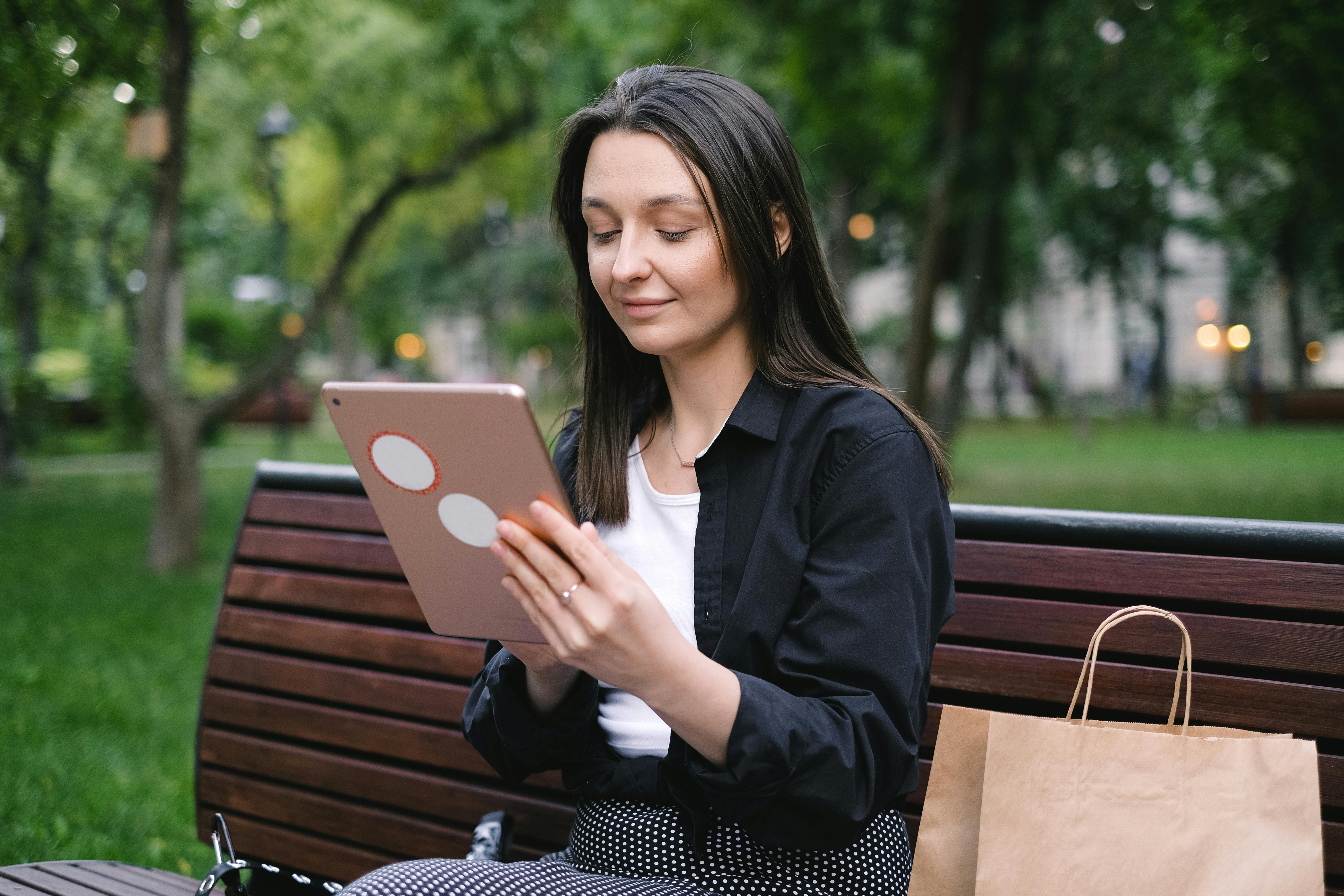 A Woman Sitting on the Bench While using Digital Tablet · Free Stock Photo