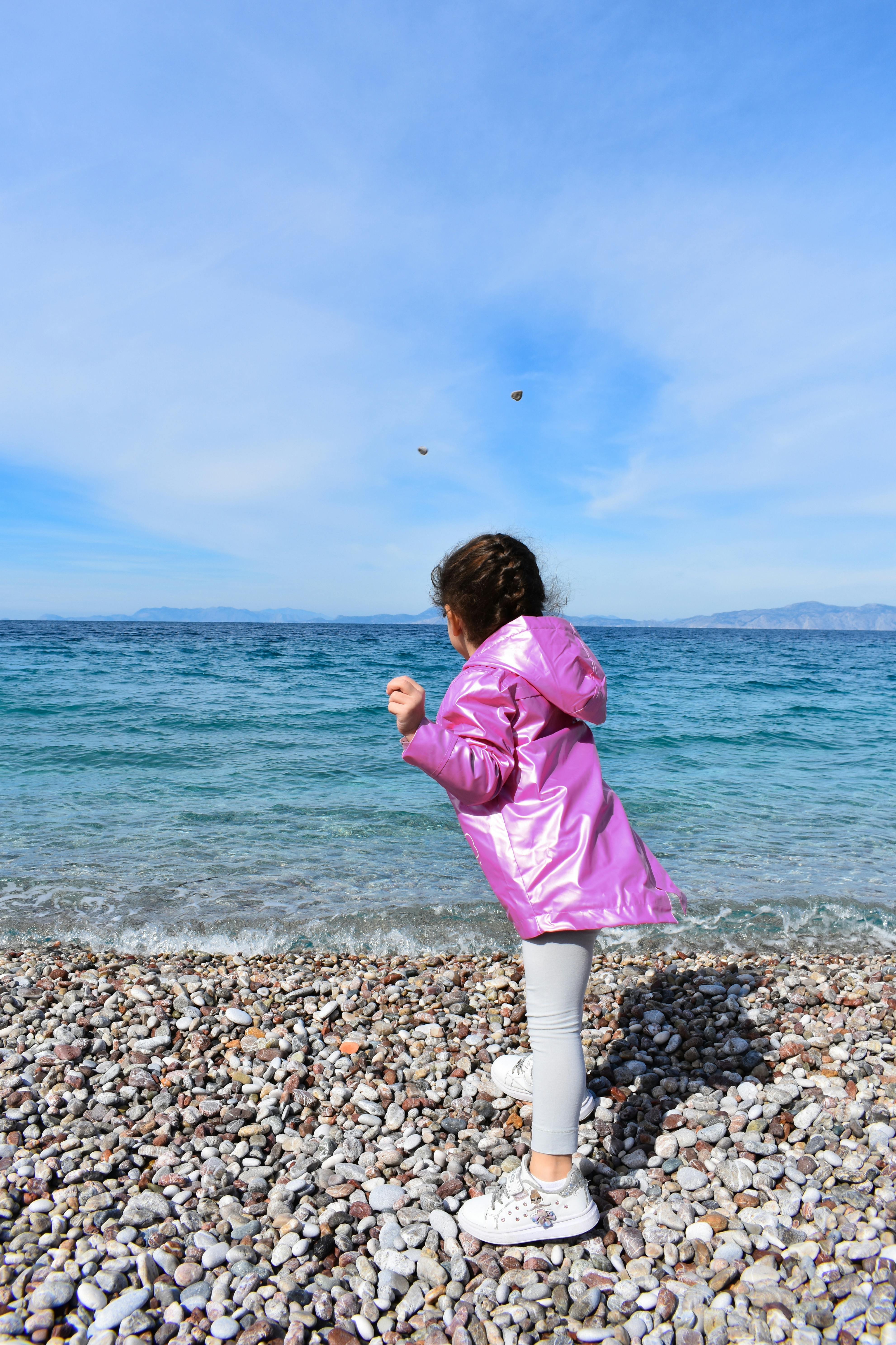 The girl is in a position of throwing a rock in the sea · Free Stock Photo