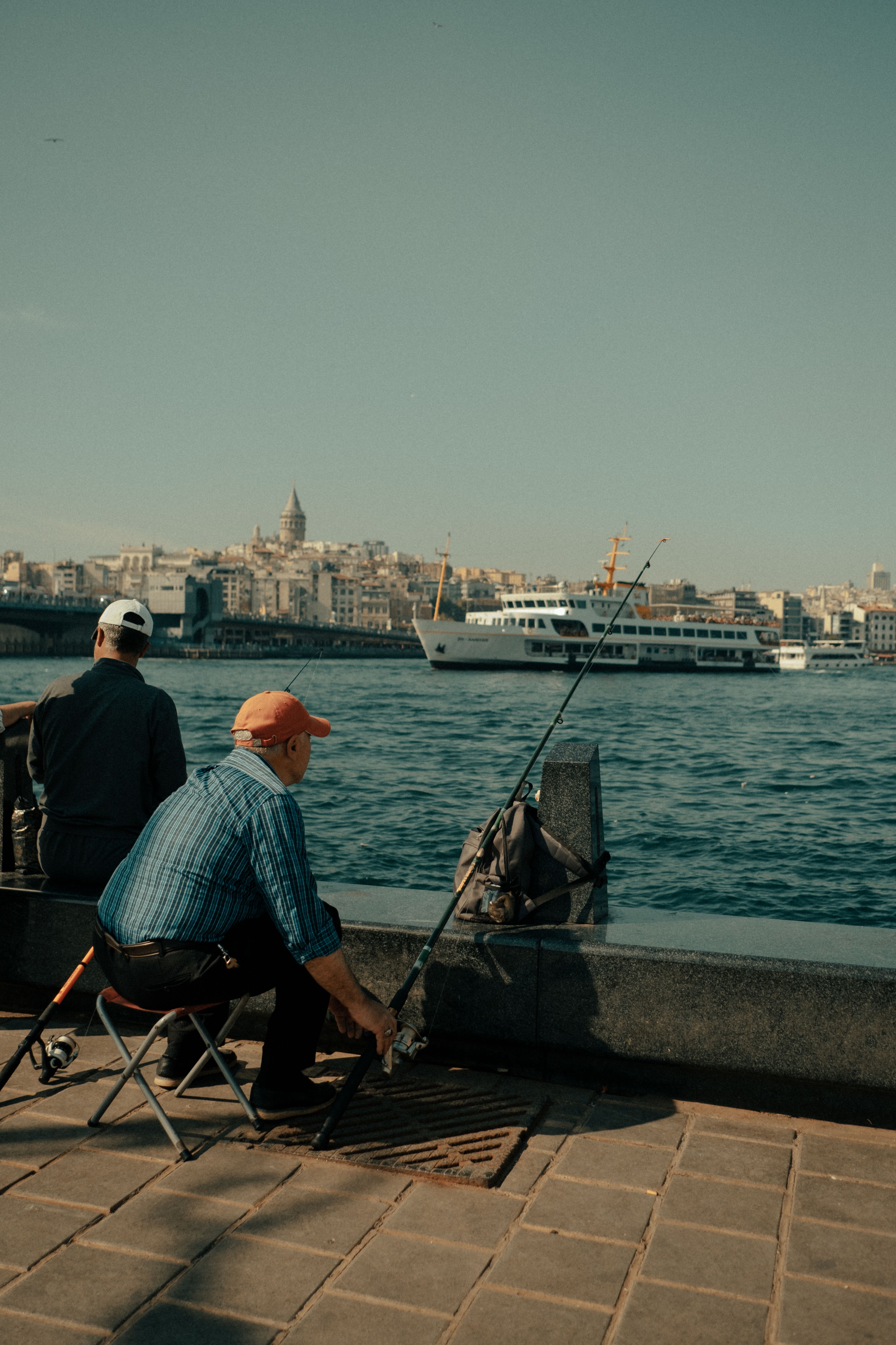 Man Fishing in a Harbor With a Ferry in the Background · Free Stock Photo