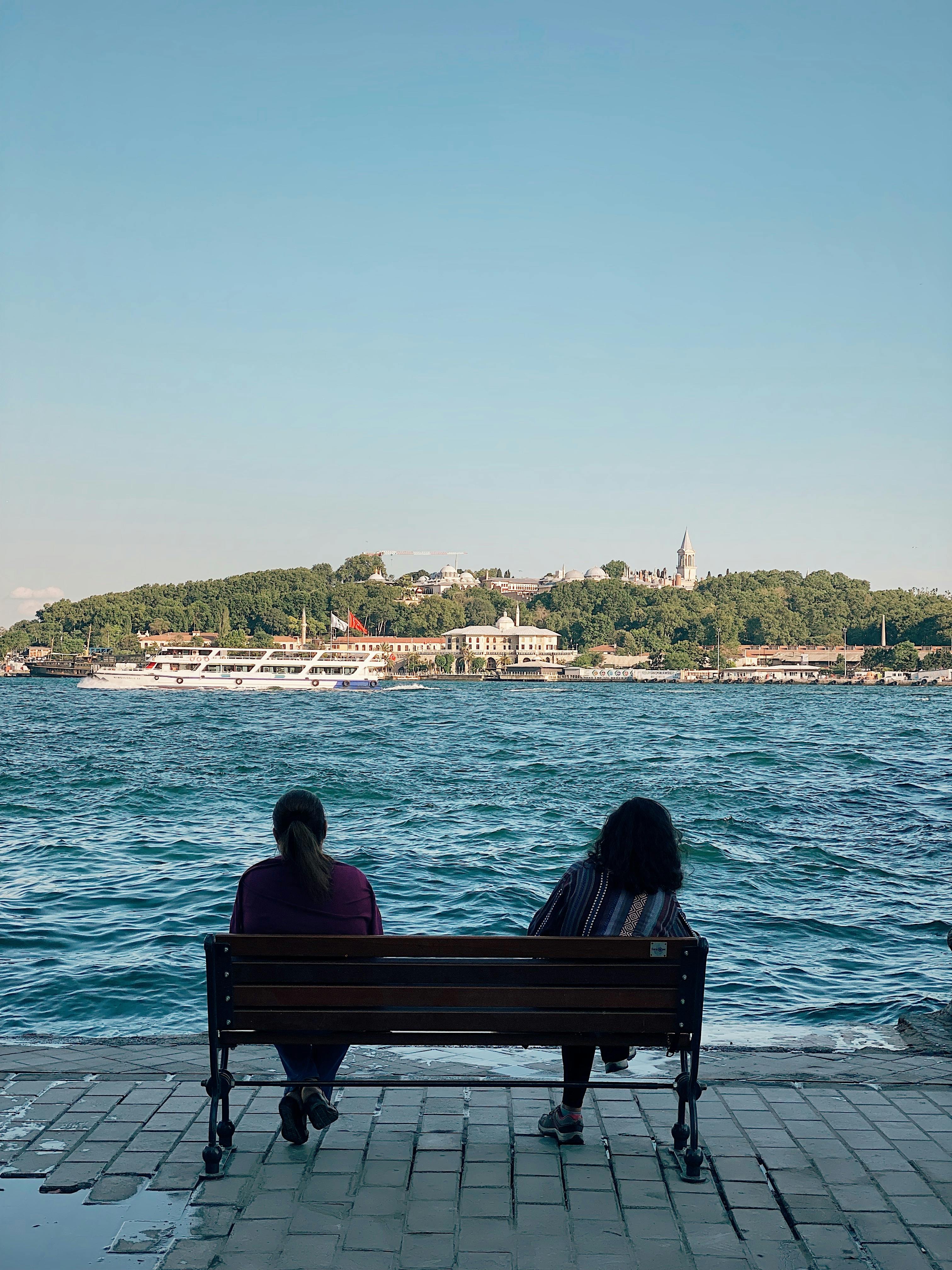 Women Sitting on Bench Facing Body of Water · Free Stock Photo