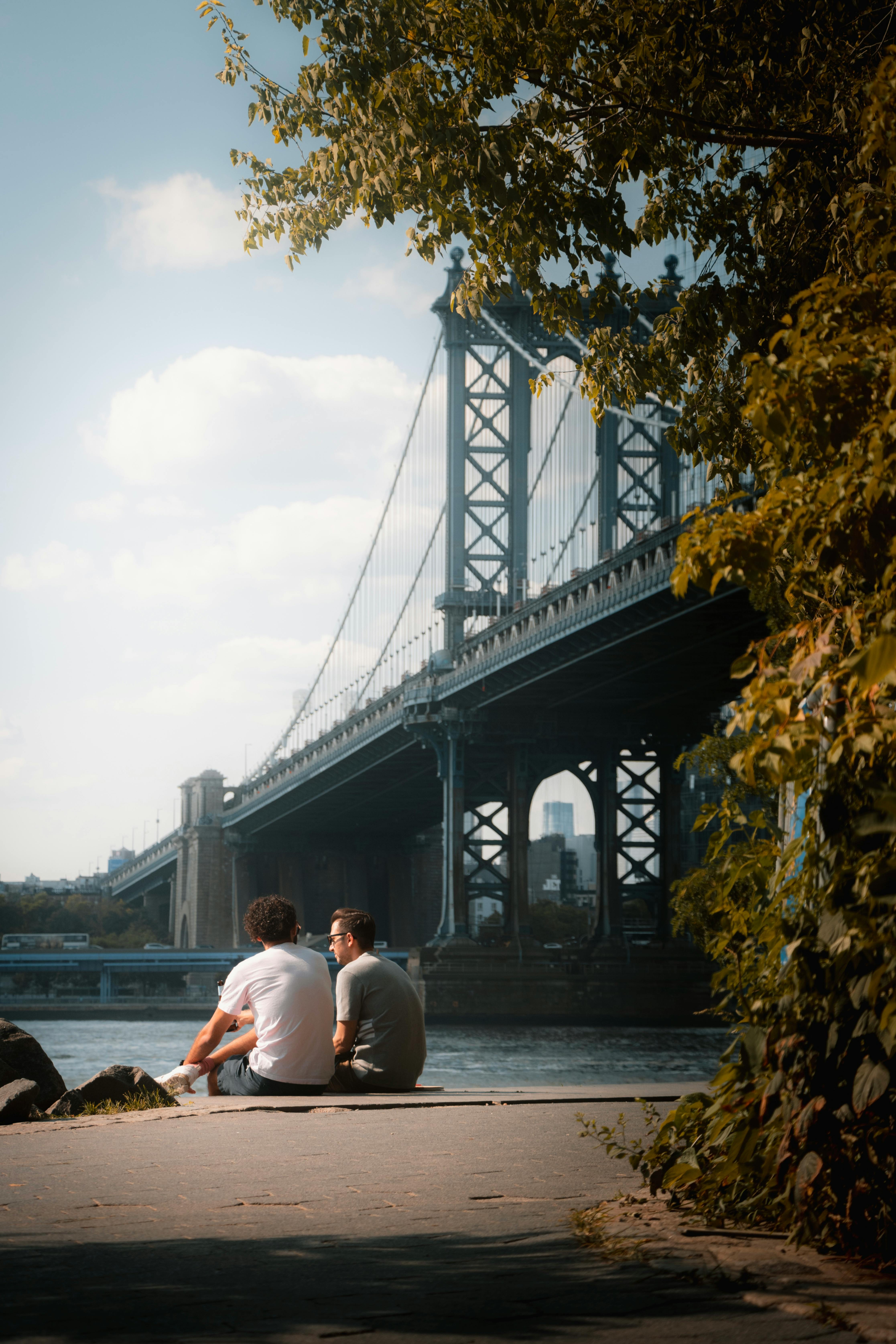 Men Sitting on River Side under Bridge · Free Stock Photo
