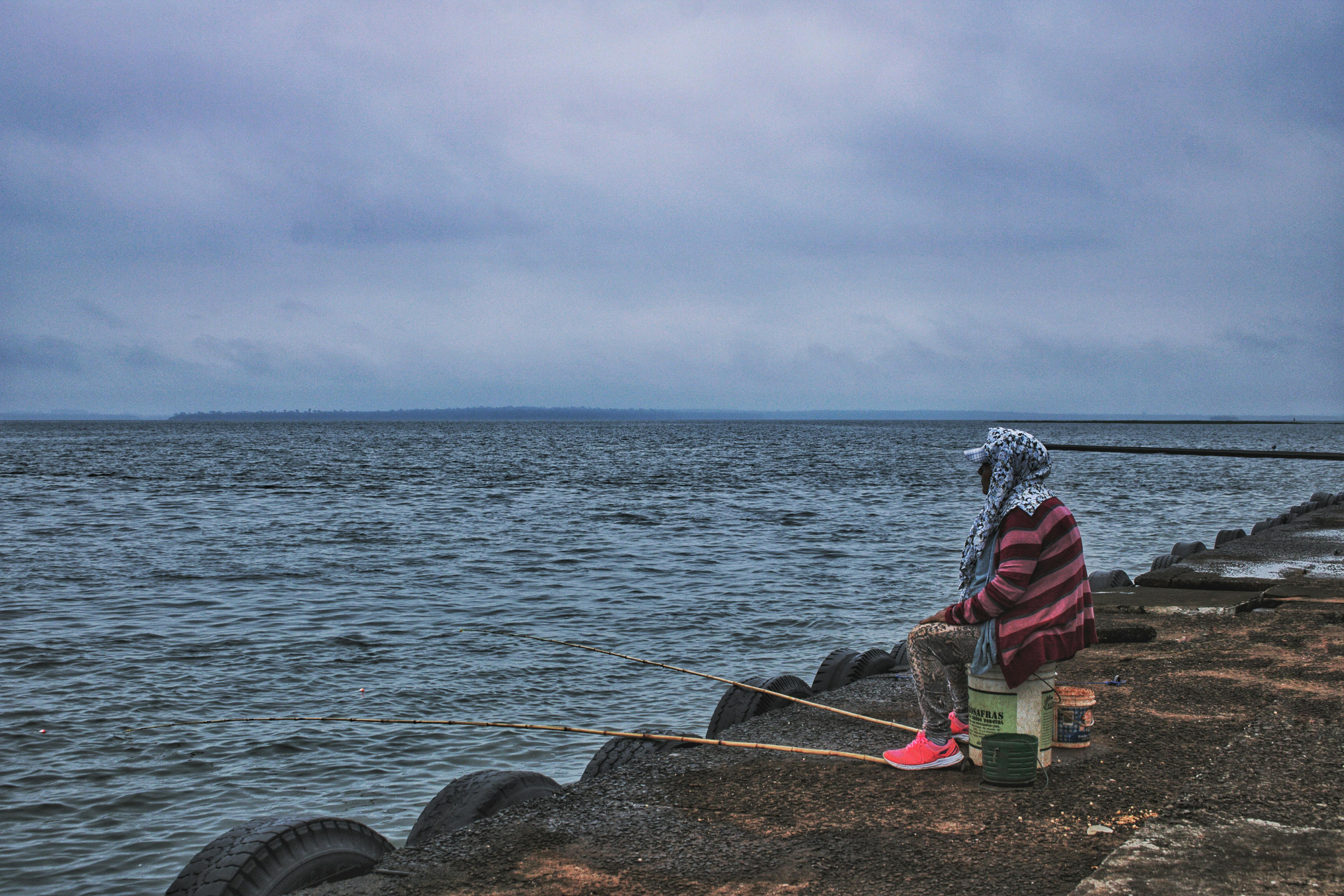 A Man Sitting on Bucket while Fishing · Free Stock Photo