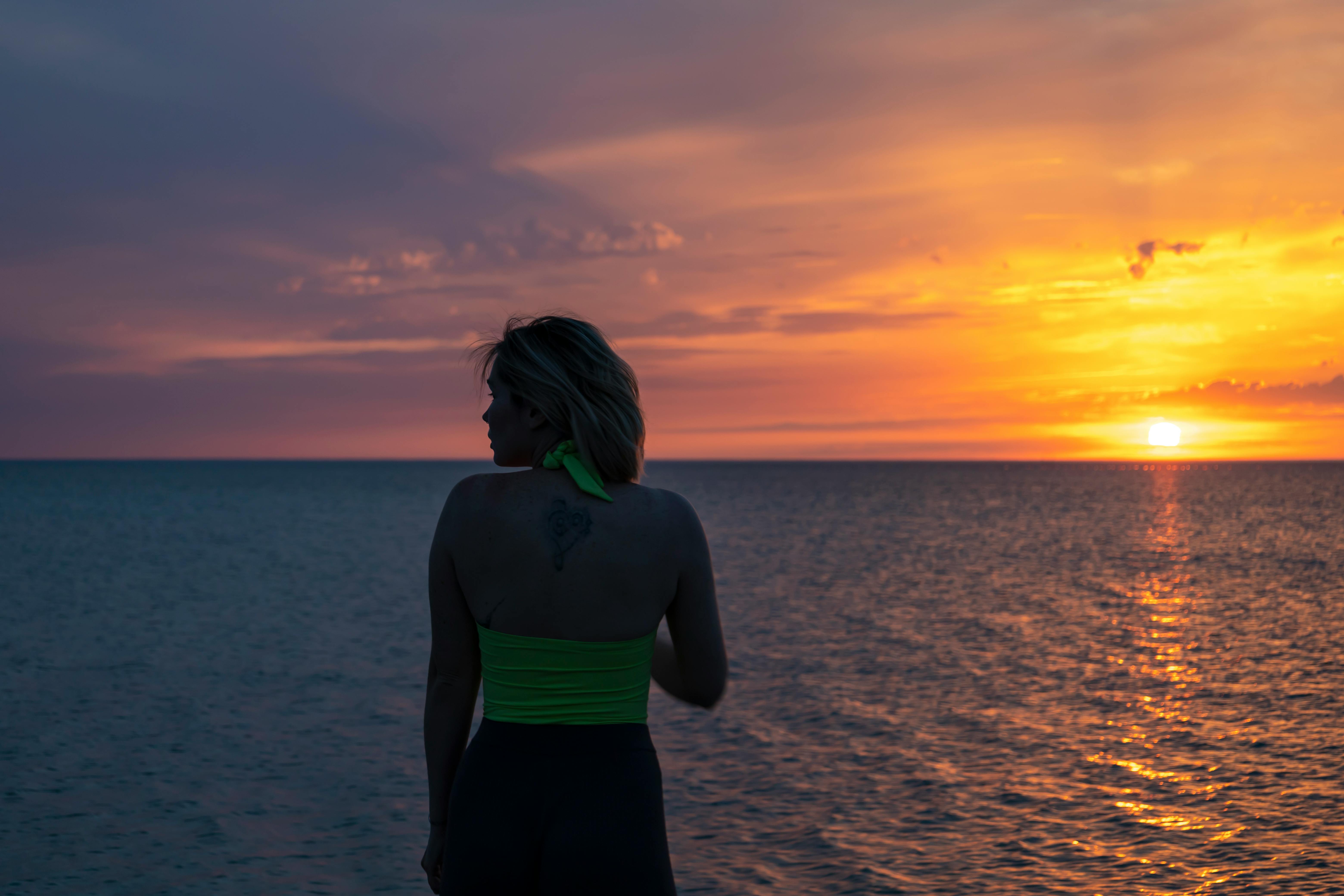 Back View of a Woman Standing Near the Sea During Sunset · Free Stock Photo