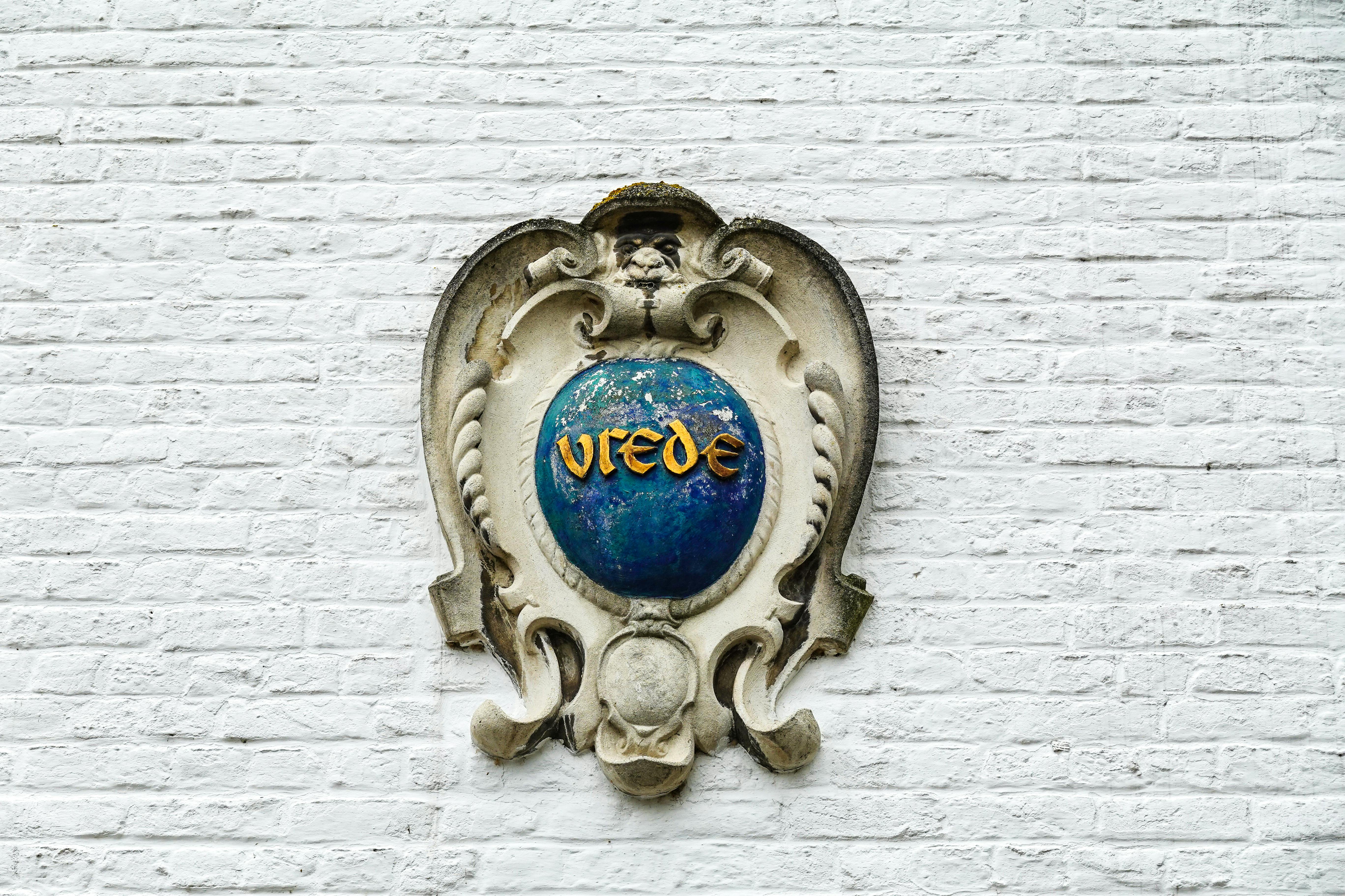 Carved Symbol with a Sign Hanging on a White Brick Wall · Free Stock Photo