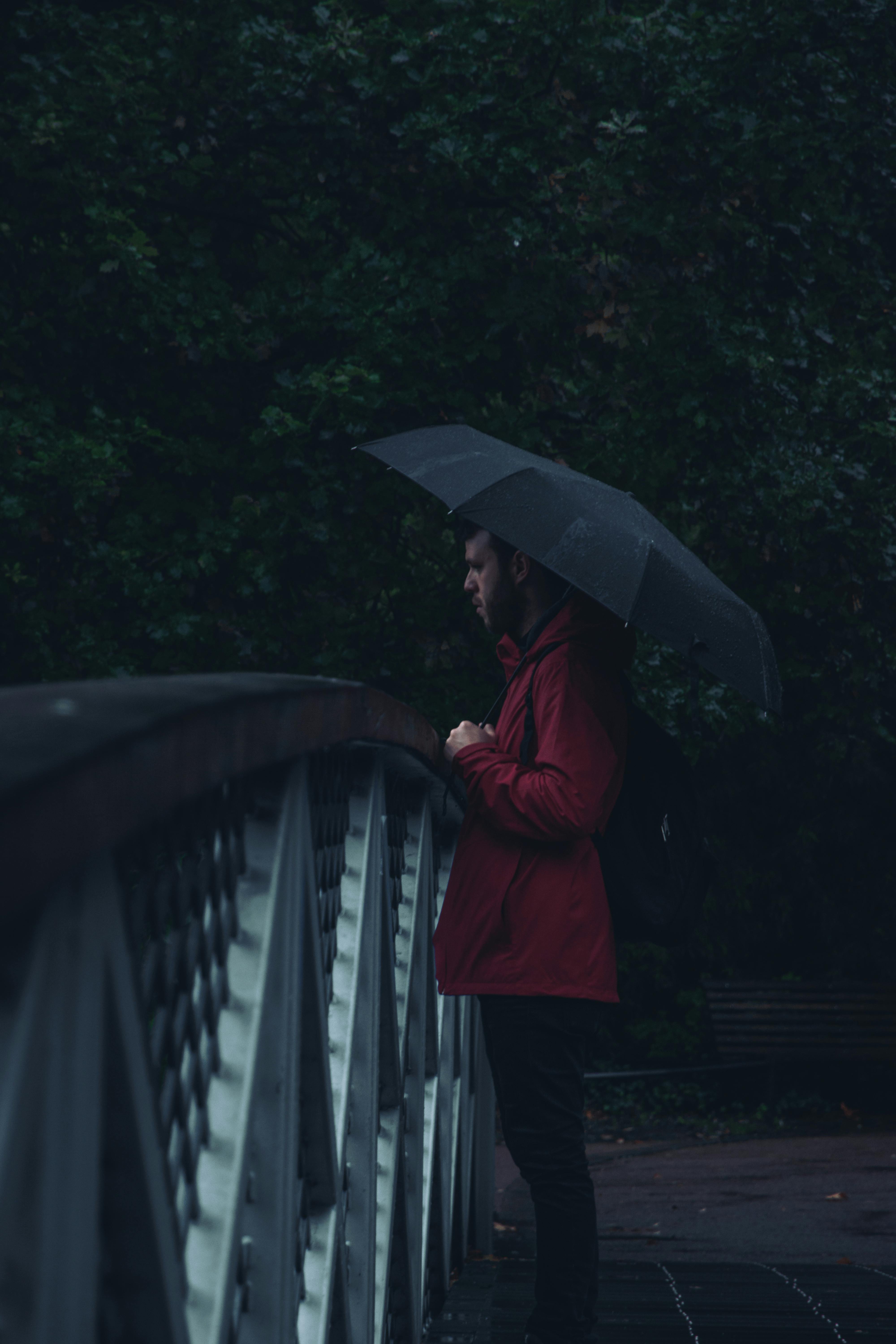 Man with an Umbrella Standing Beside a Metal railing · Free Stock Photo