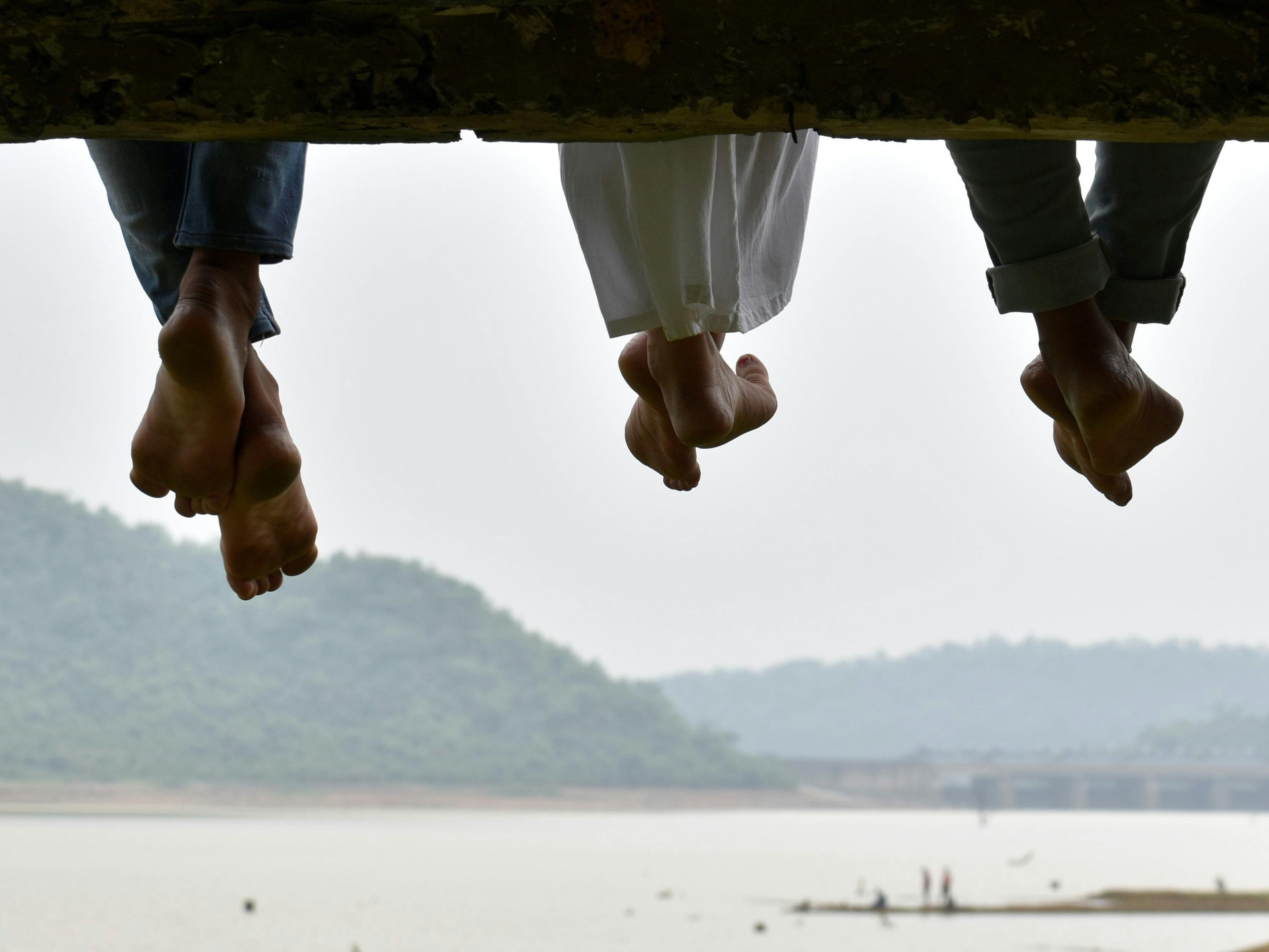 Legs Hanging against River among Hills · Free Stock Photo