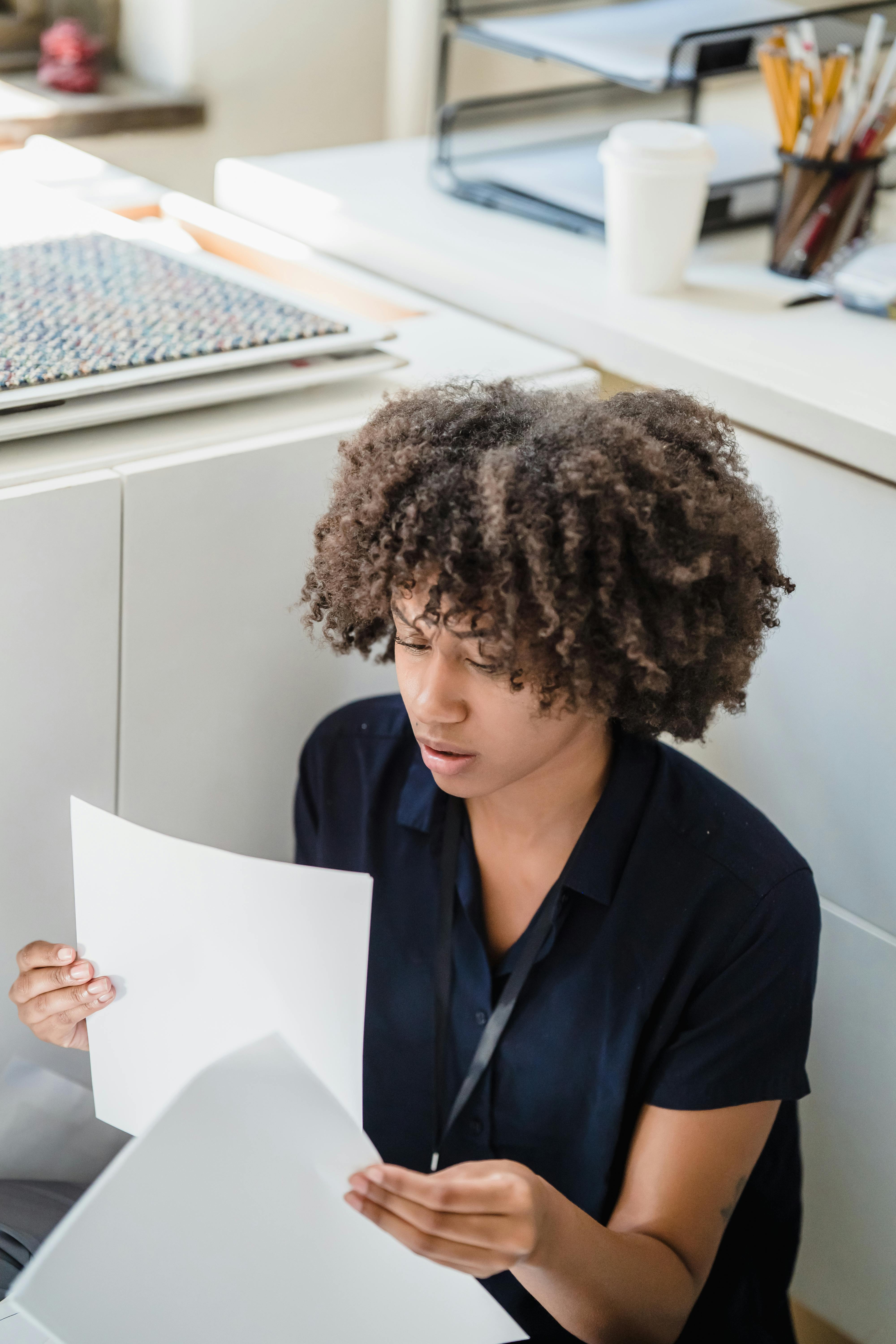 Confused Female Office Worker Crouching at a Desk · Free Stock Photo