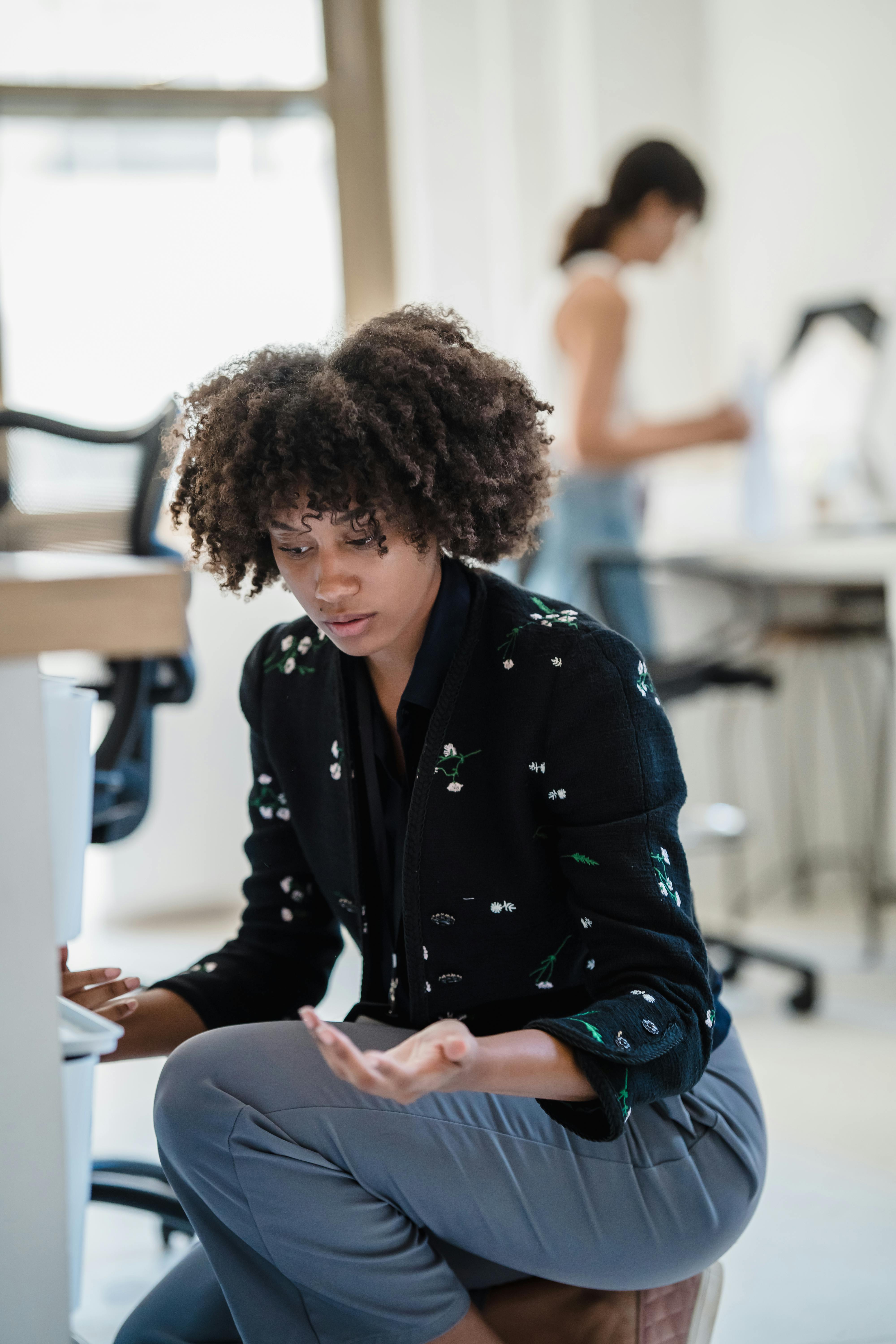 Confused Female Office Worker Crouching at a Desk · Free Stock Photo