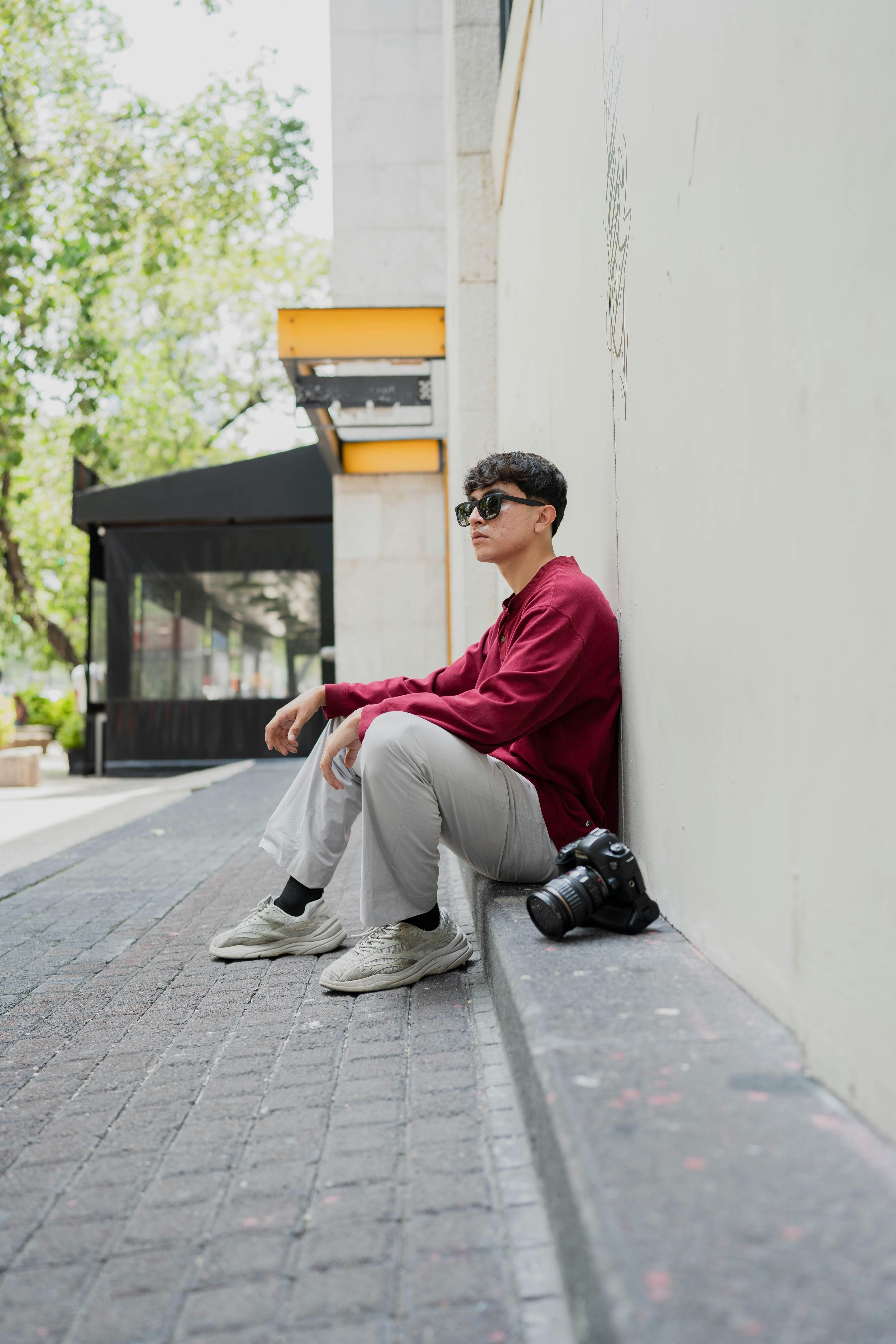 Man in Red Sweatshirt Sitting Beside a Wall · Free Stock Photo