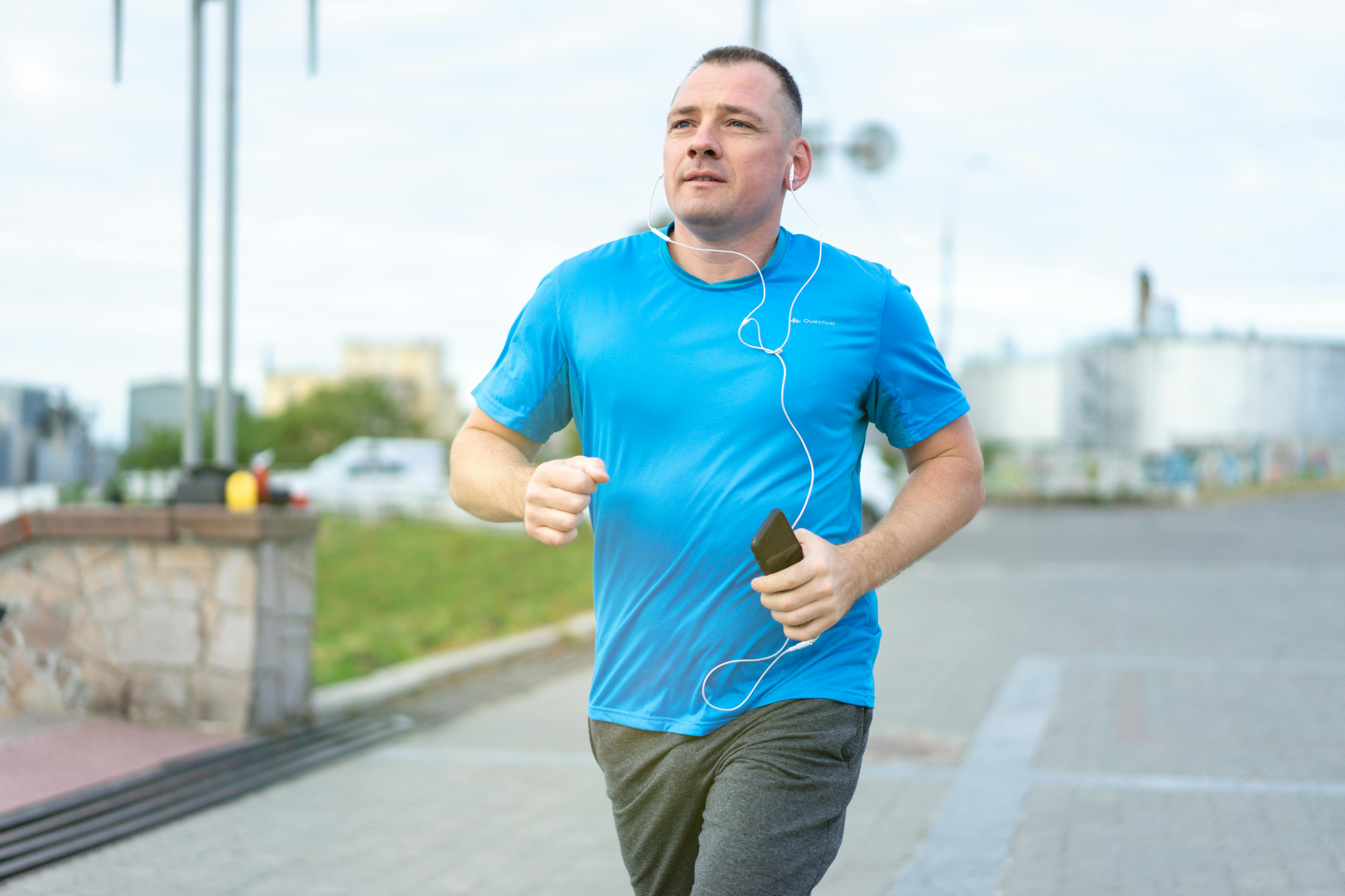 Photo of Woman Listening to Music on Earphones Jogging Down a Paved ...