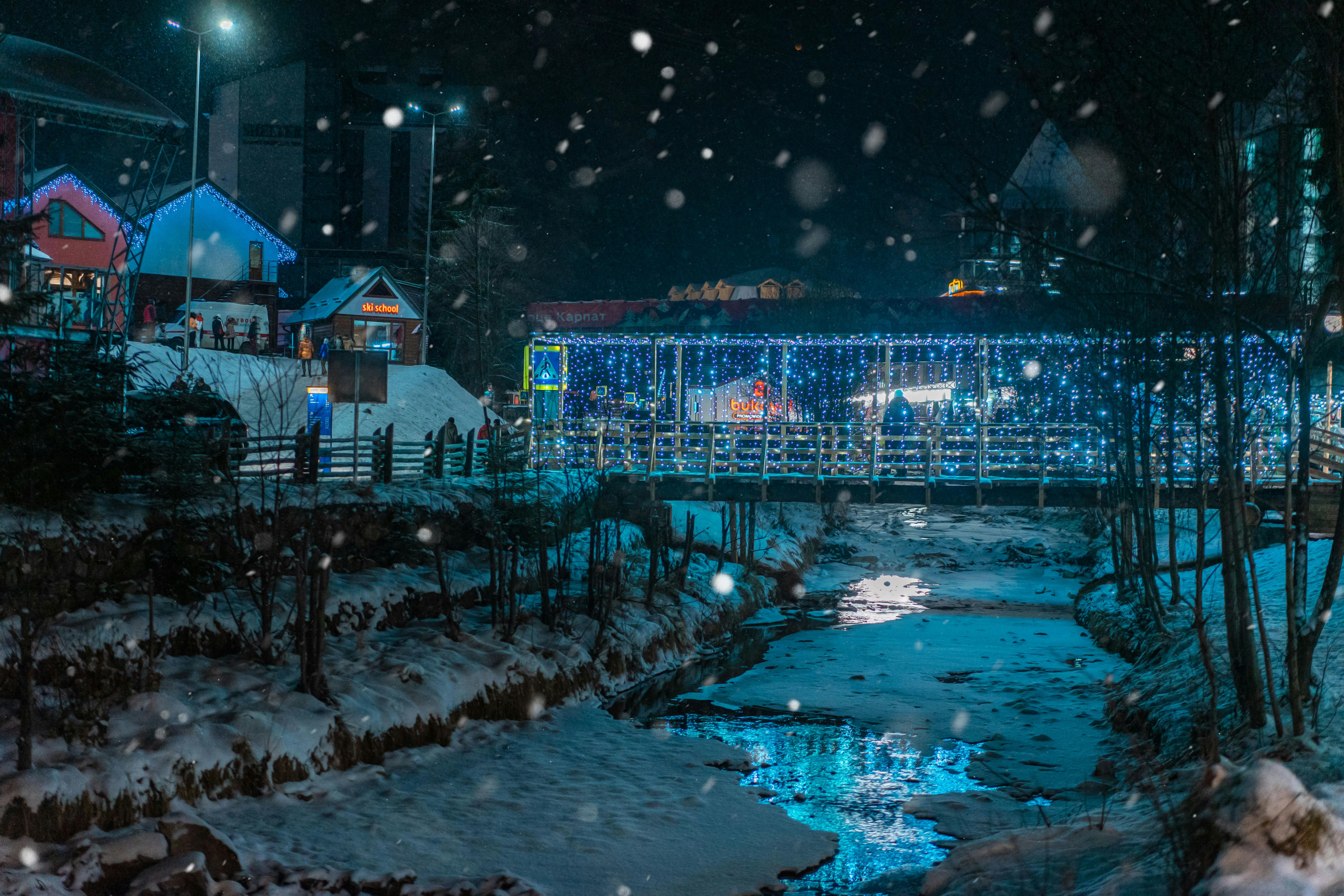 Bridge with String Lights Above a Snow Covered River at Night Time ...