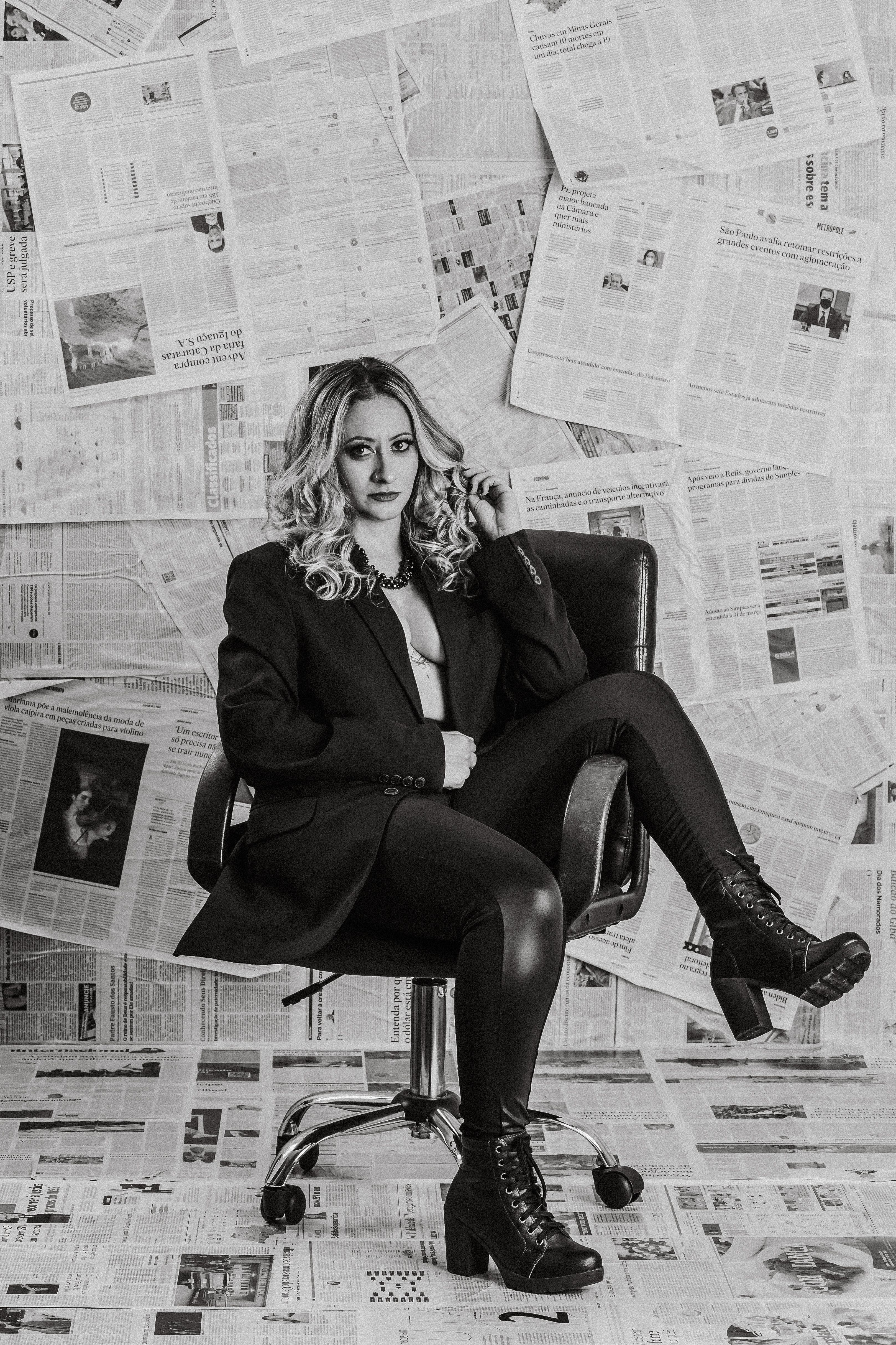 A Greyscale Photo of a Woman Sitting Infront of a Newspaper Background ...