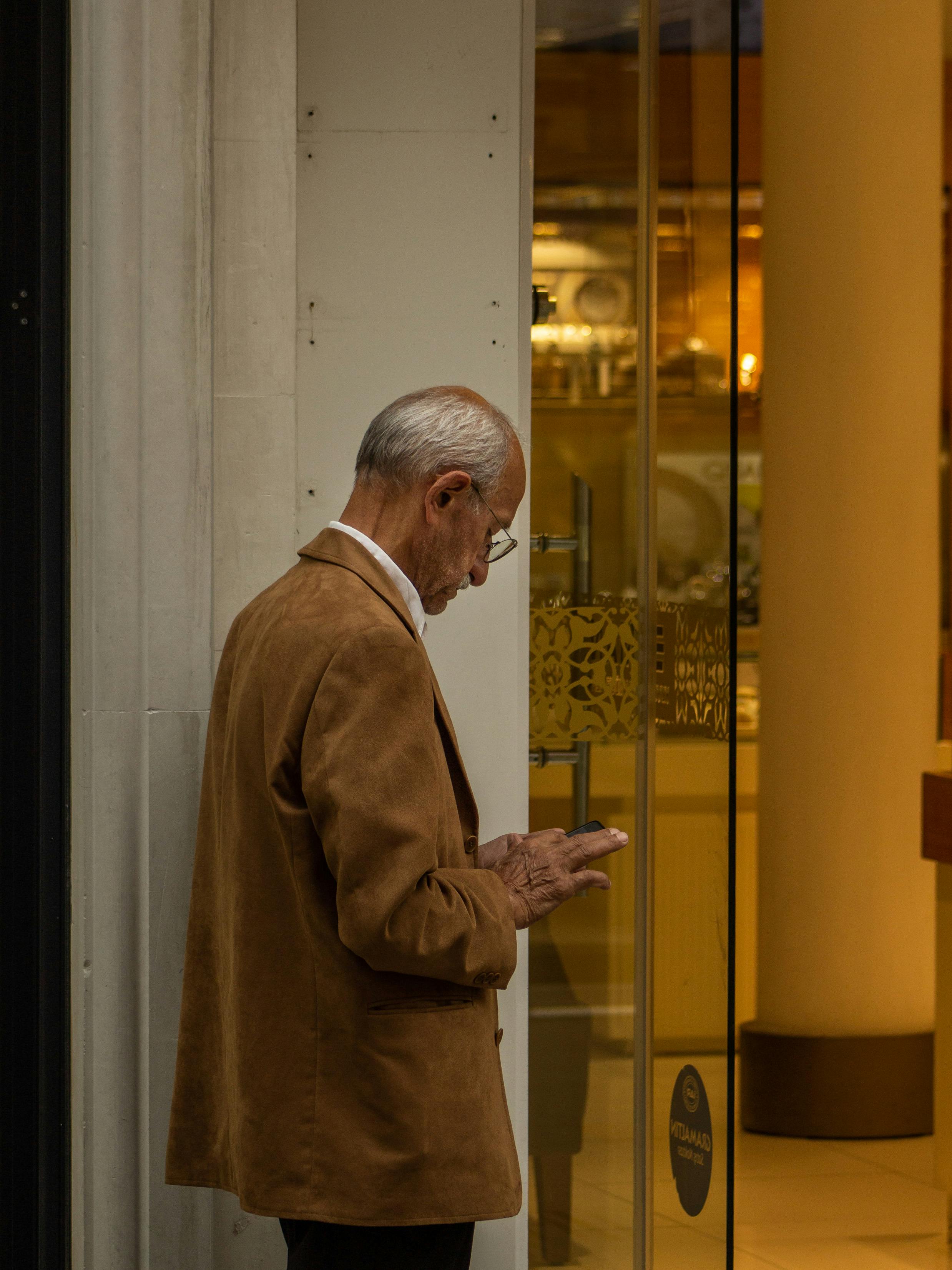 Young Man Waiting by a Beige Building Entrance and Checking Phone ...