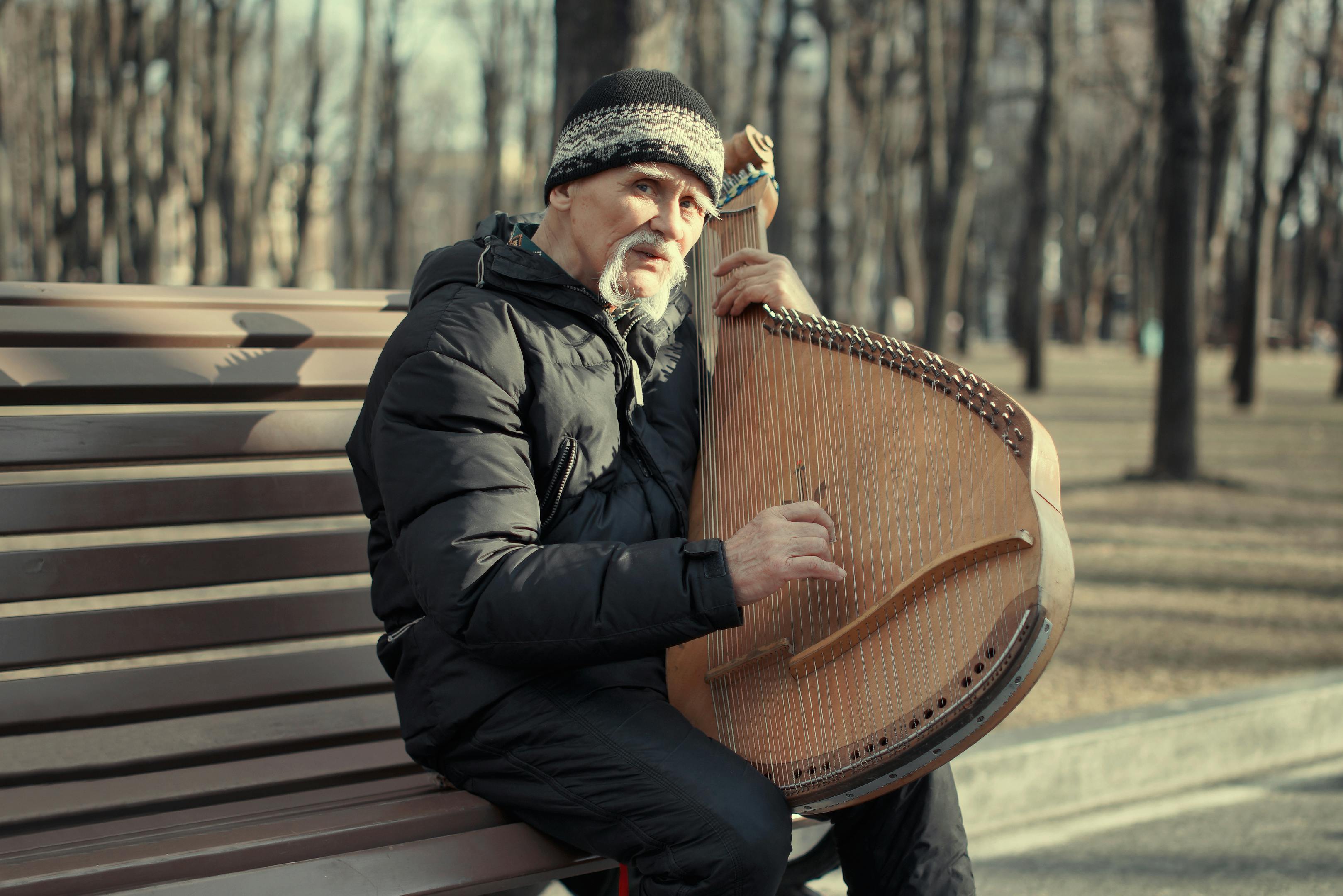 A Man in Black Leather Jacket Sitting on Wooden Bench Playing a ...